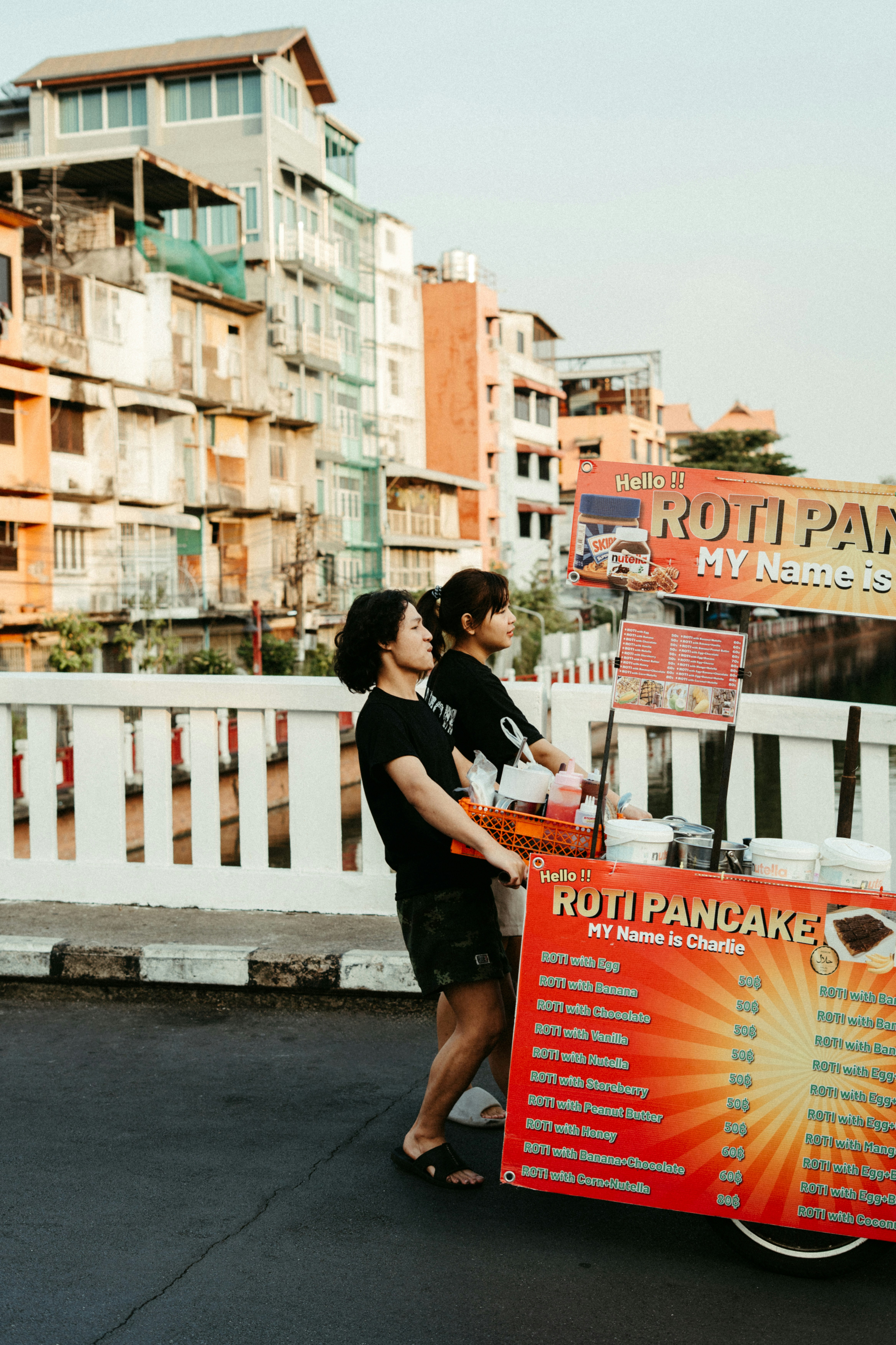 Two women push a food cart down the street.