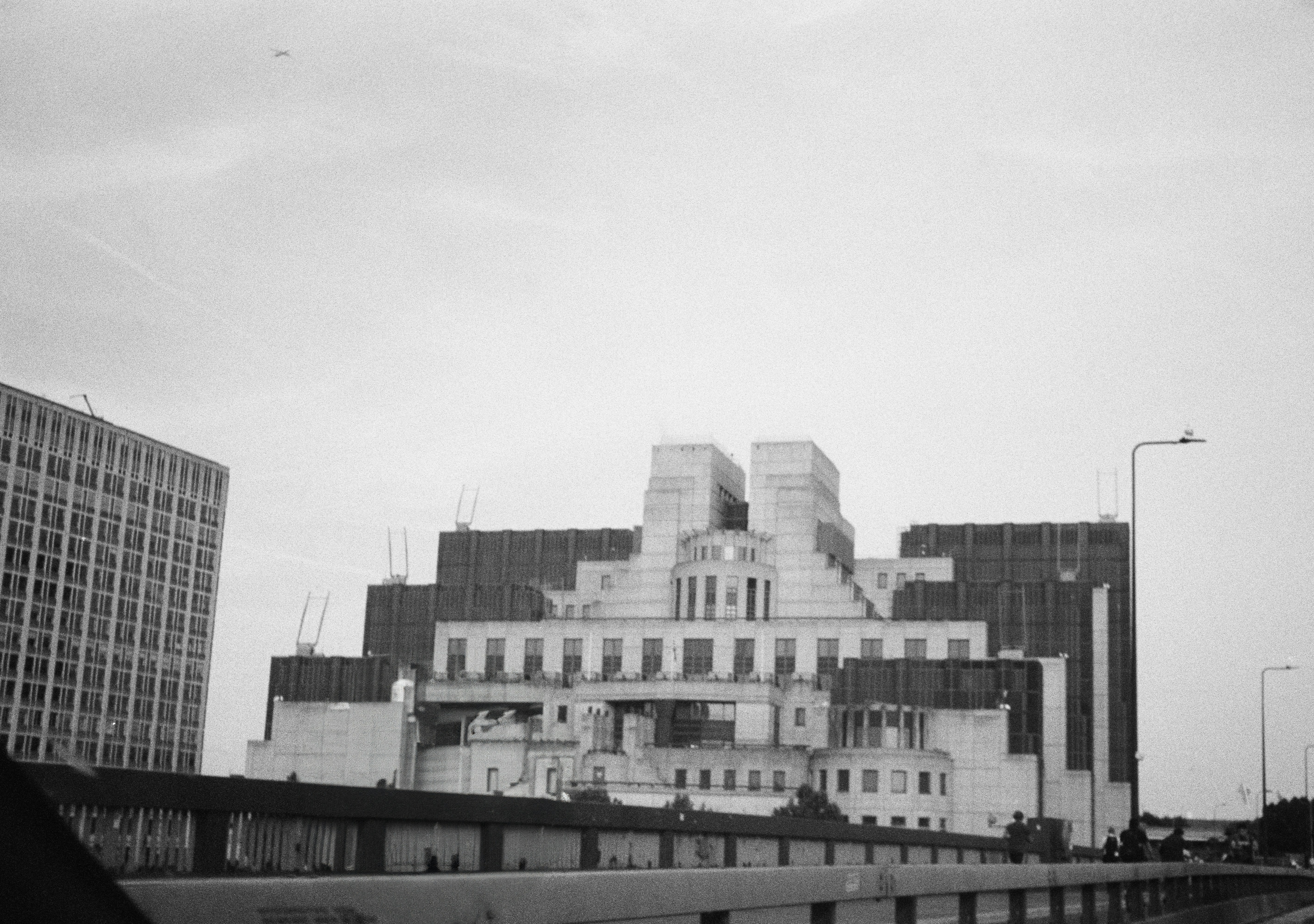 The iconic MI6 building stands prominently against a backdrop of urban architecture, showcasing its distinctive design amidst a gray sky.