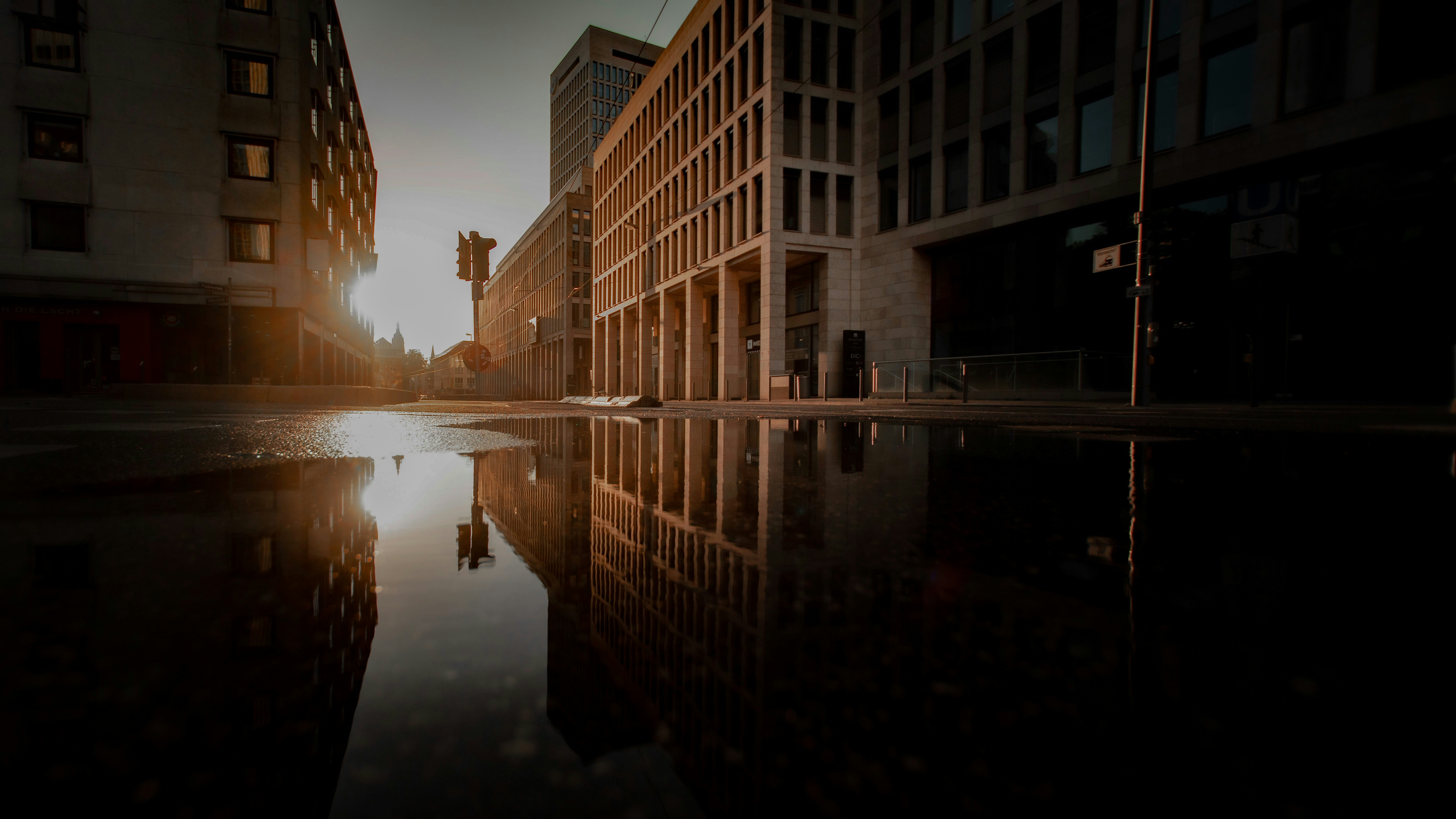Buildings reflect in a puddle at sunrise.