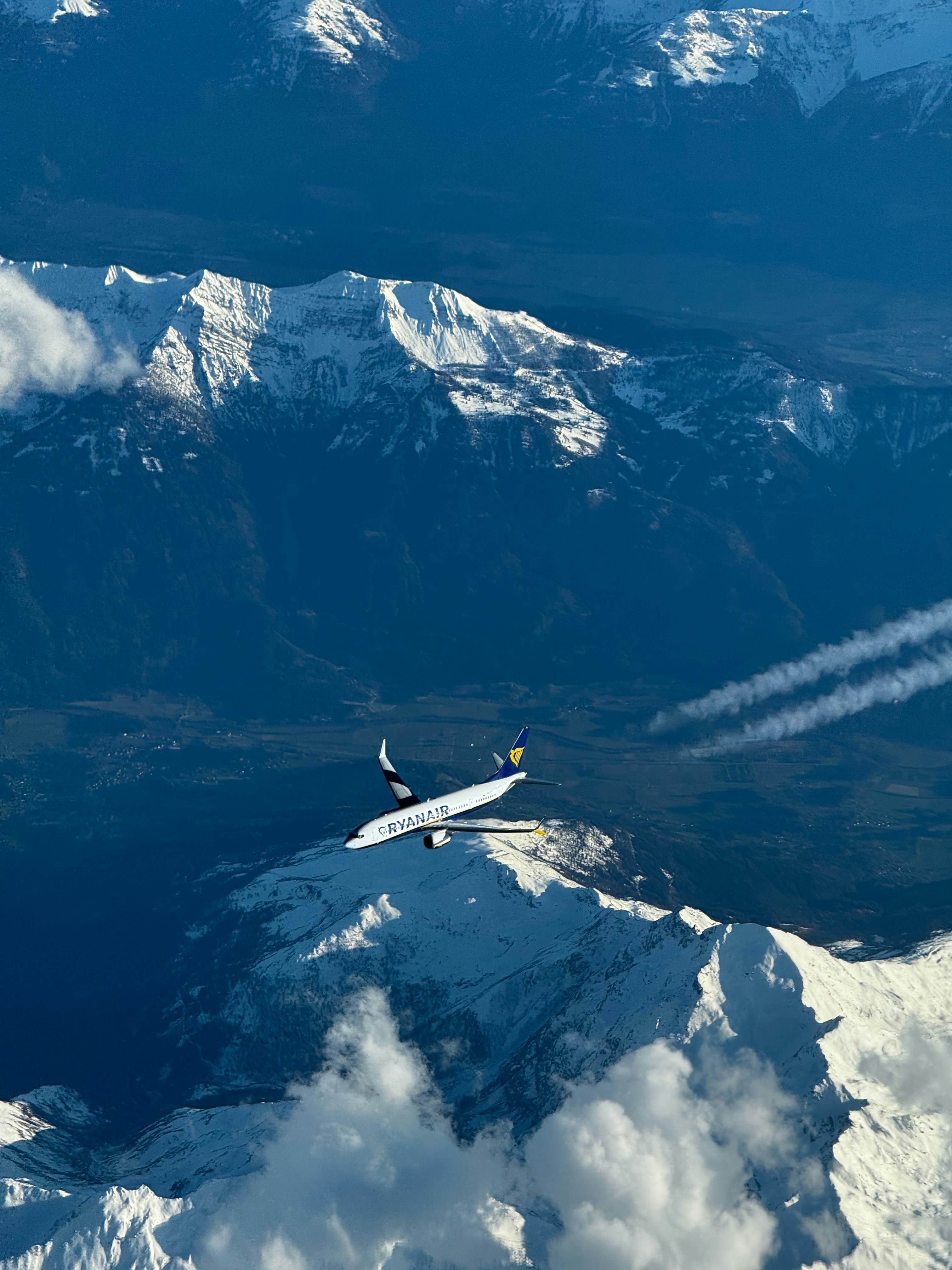 Airplane flies above snow-capped mountains.