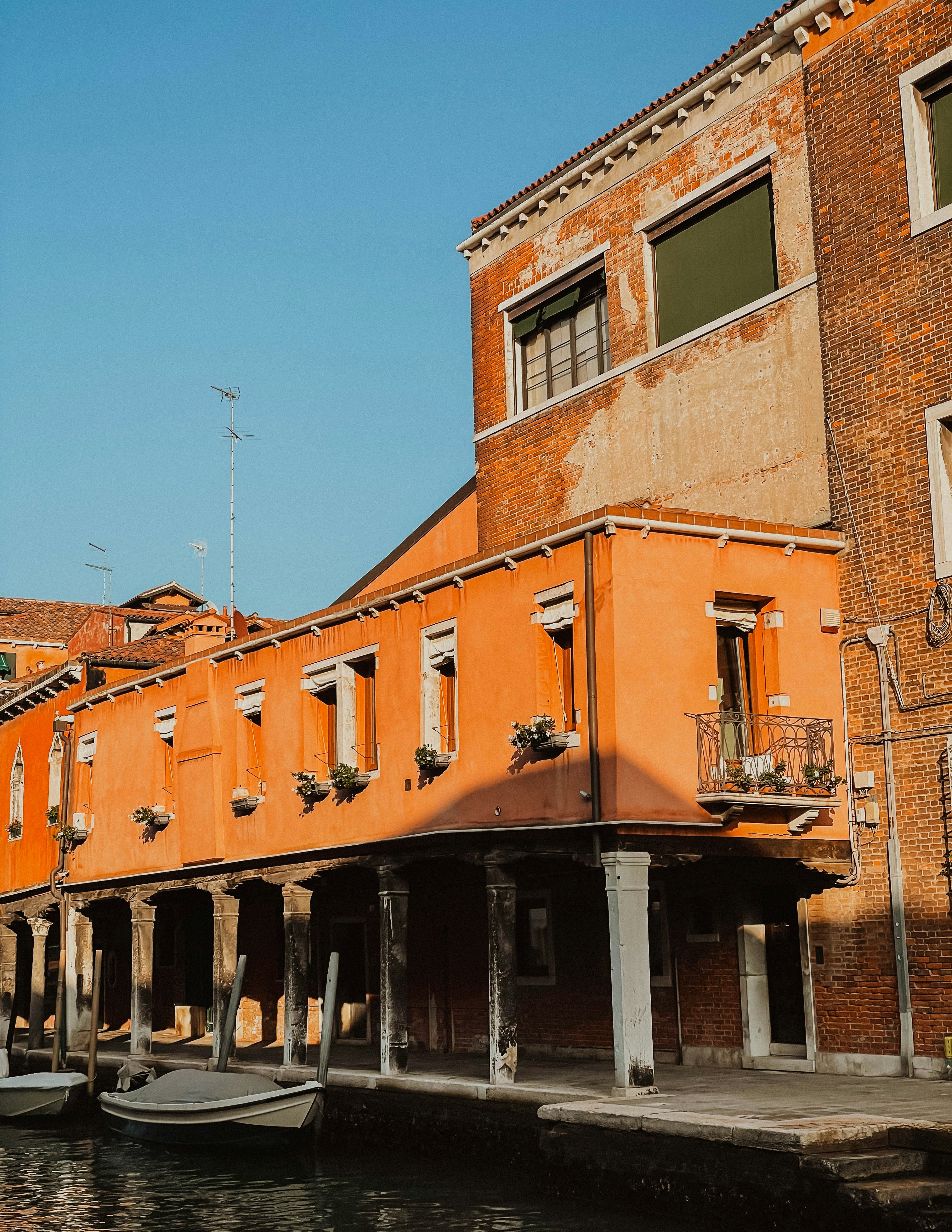 Colorful orange buildings with flower boxes line a canal in Venice, showcasing the unique architecture and serene waterway.