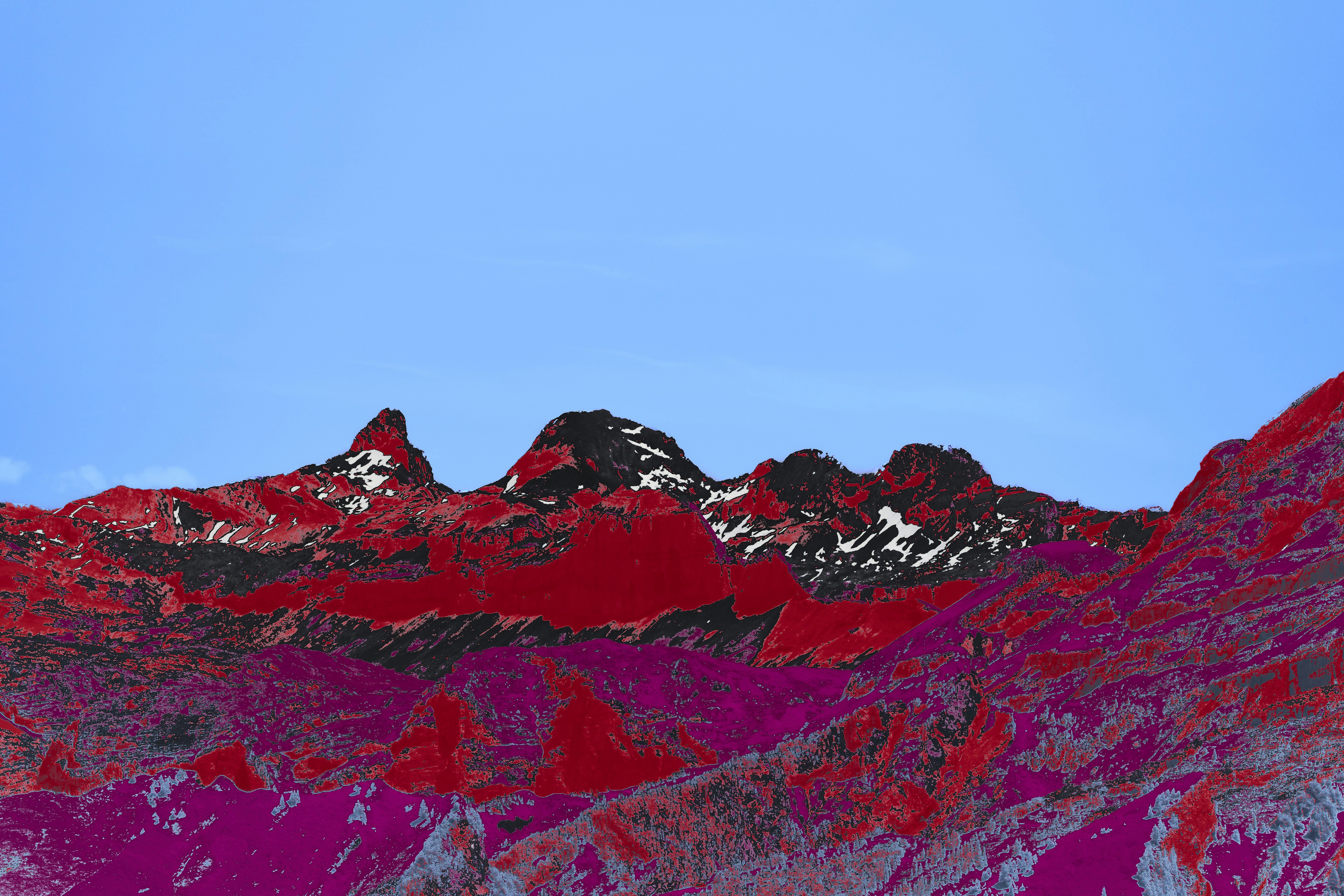 Vibrant mountain range rendered in striking red and purple hues, contrasting against a clear blue sky. The surreal colors create a dreamlike landscape.