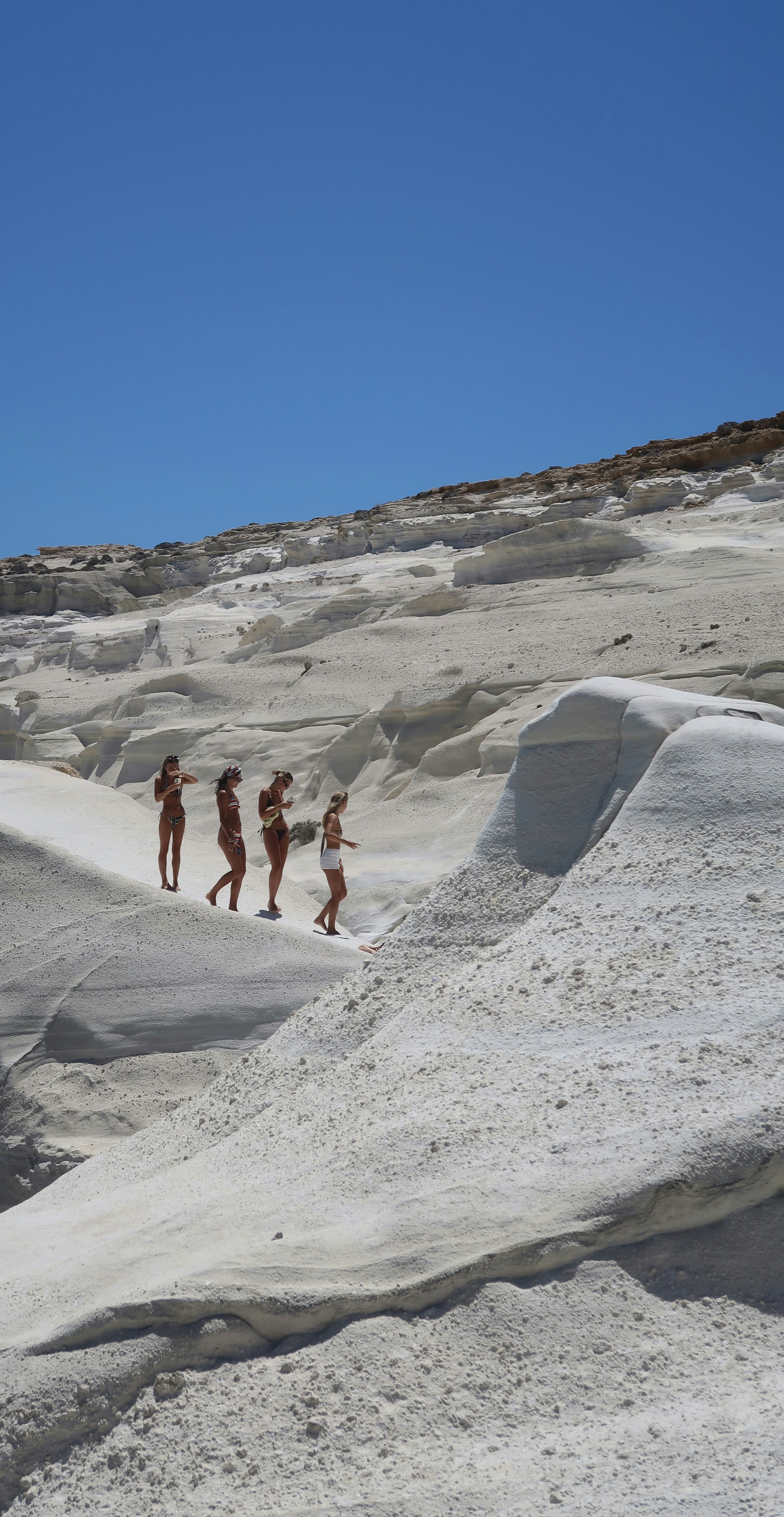Four women walk on a white, layered rock formation.