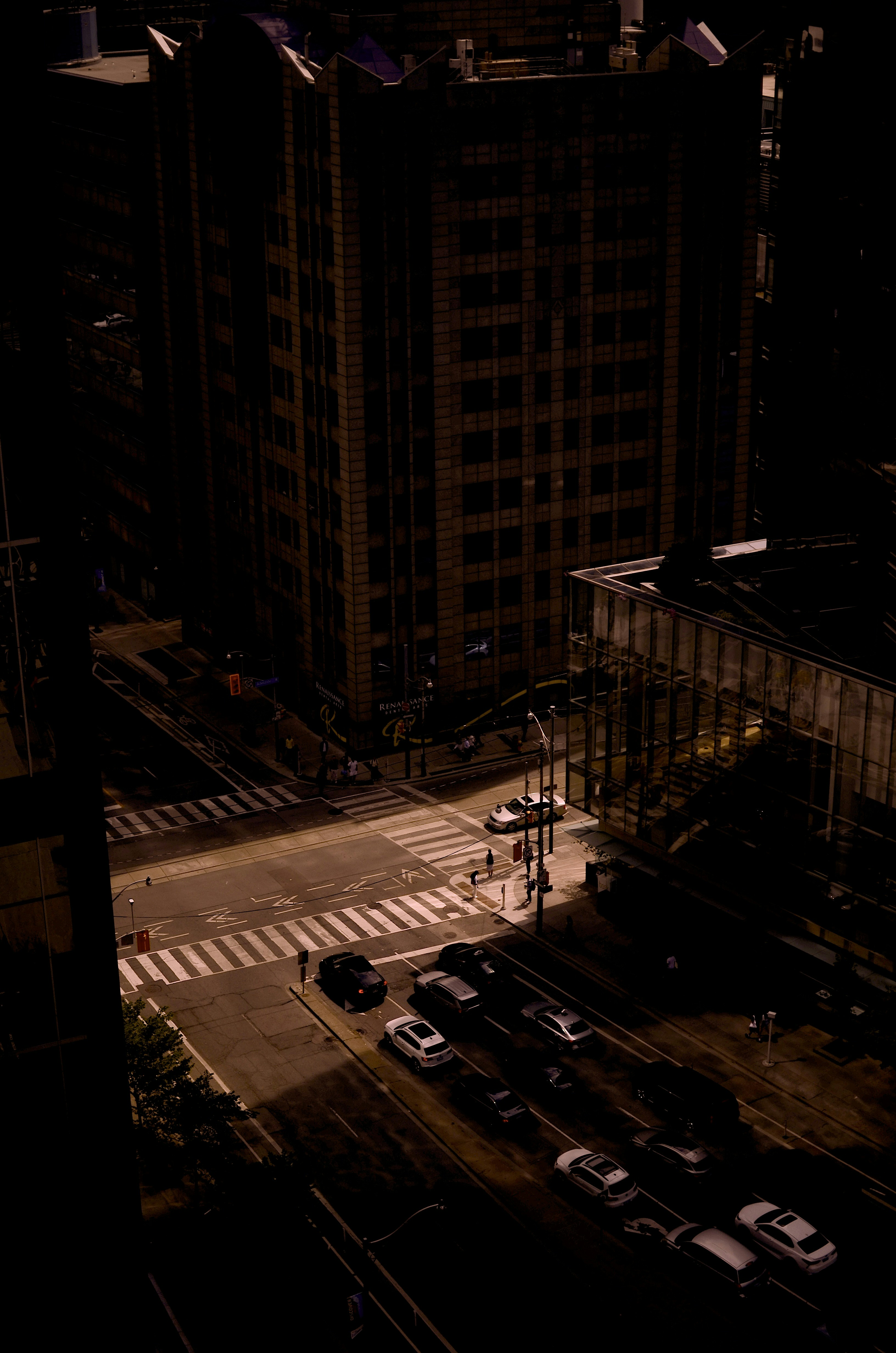 A view of a traffic intersection in downtown toronto, during golden hour as the sun sets between some buildings. | Dark city buildings with sparse street lights.