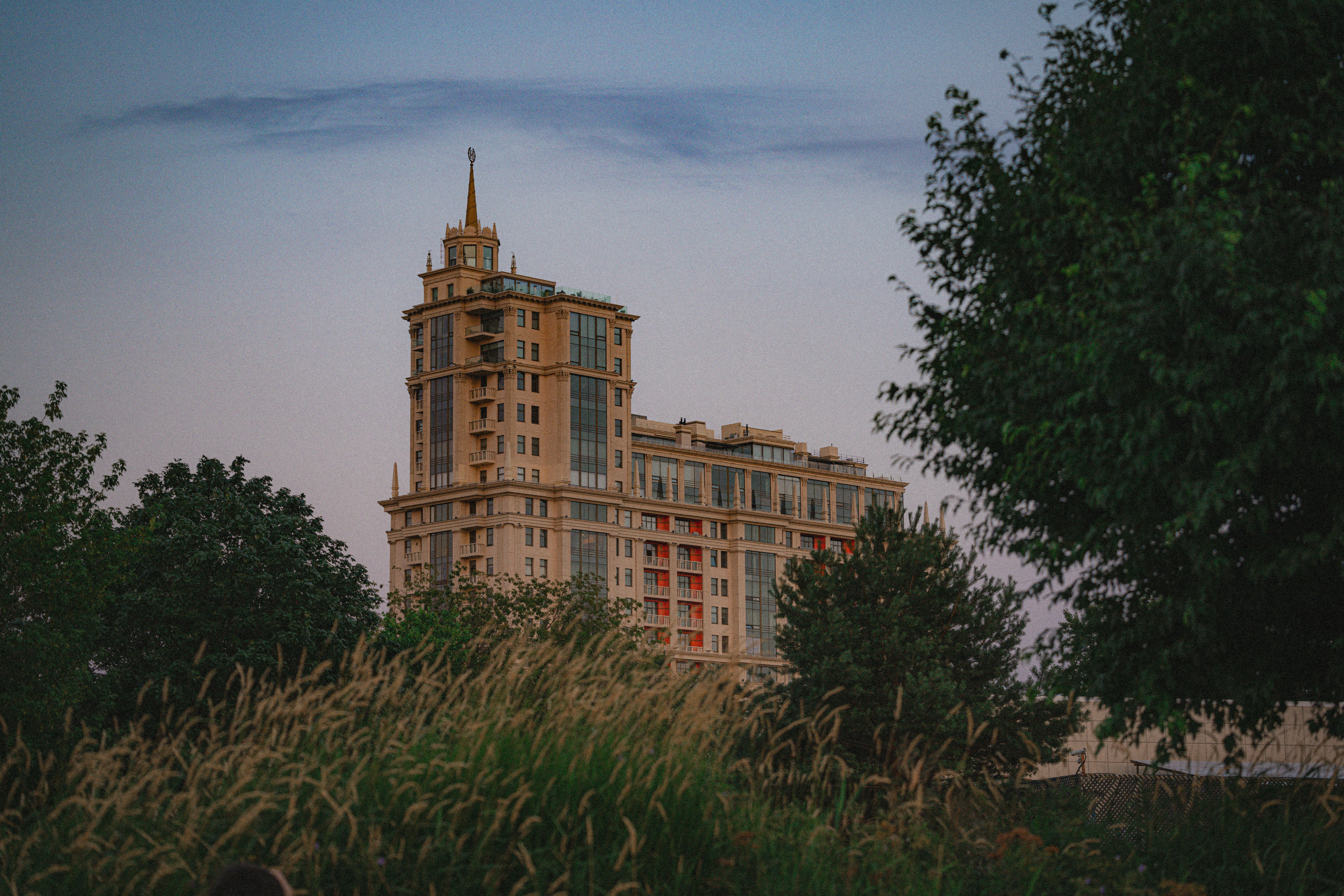 A tall, modern building rises above lush greenery, showcasing the contrast between urban architecture and natural surroundings.