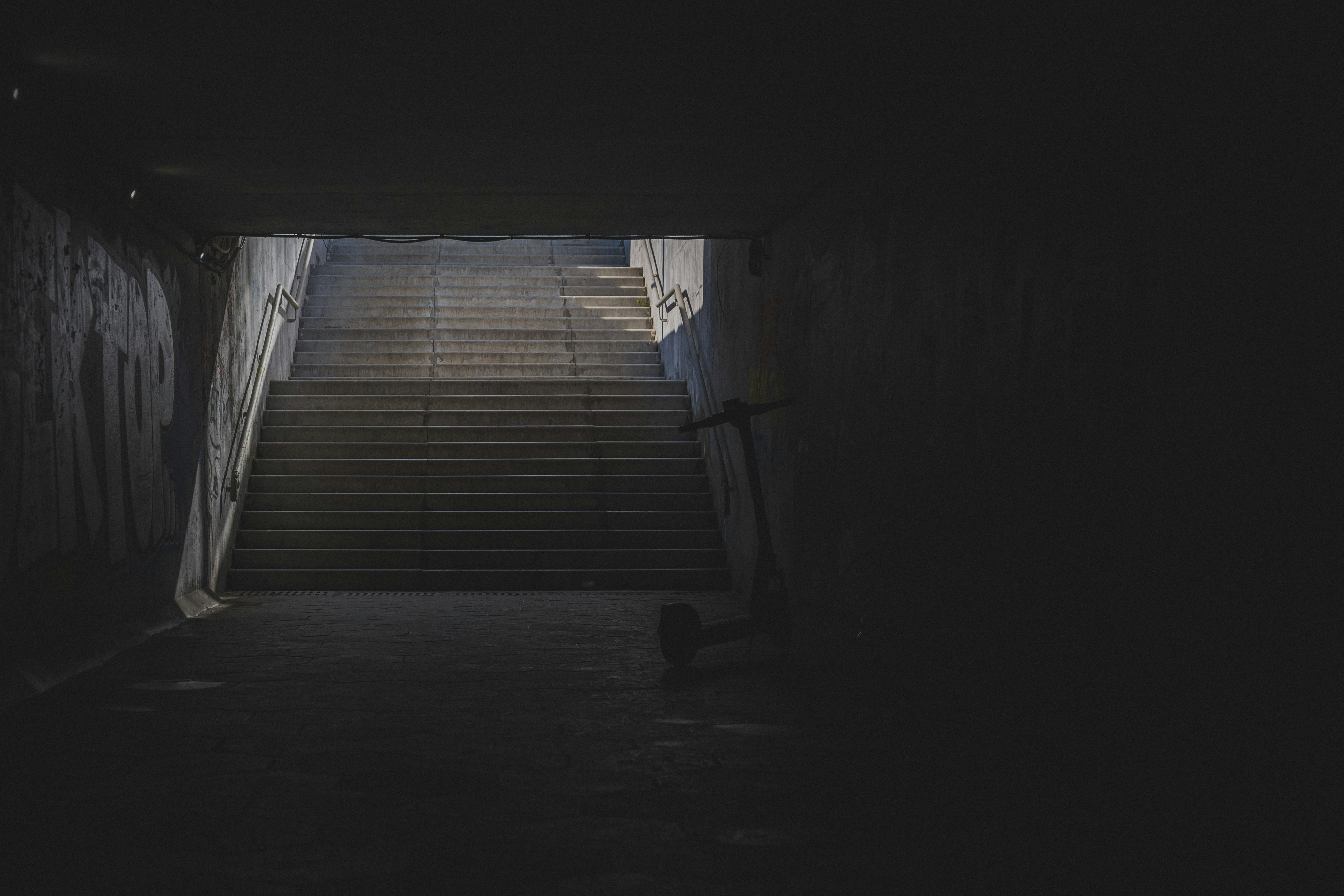 An underground pedestrian crossing with an electric scooter parked in it | Staircase leading out of a dark tunnel.