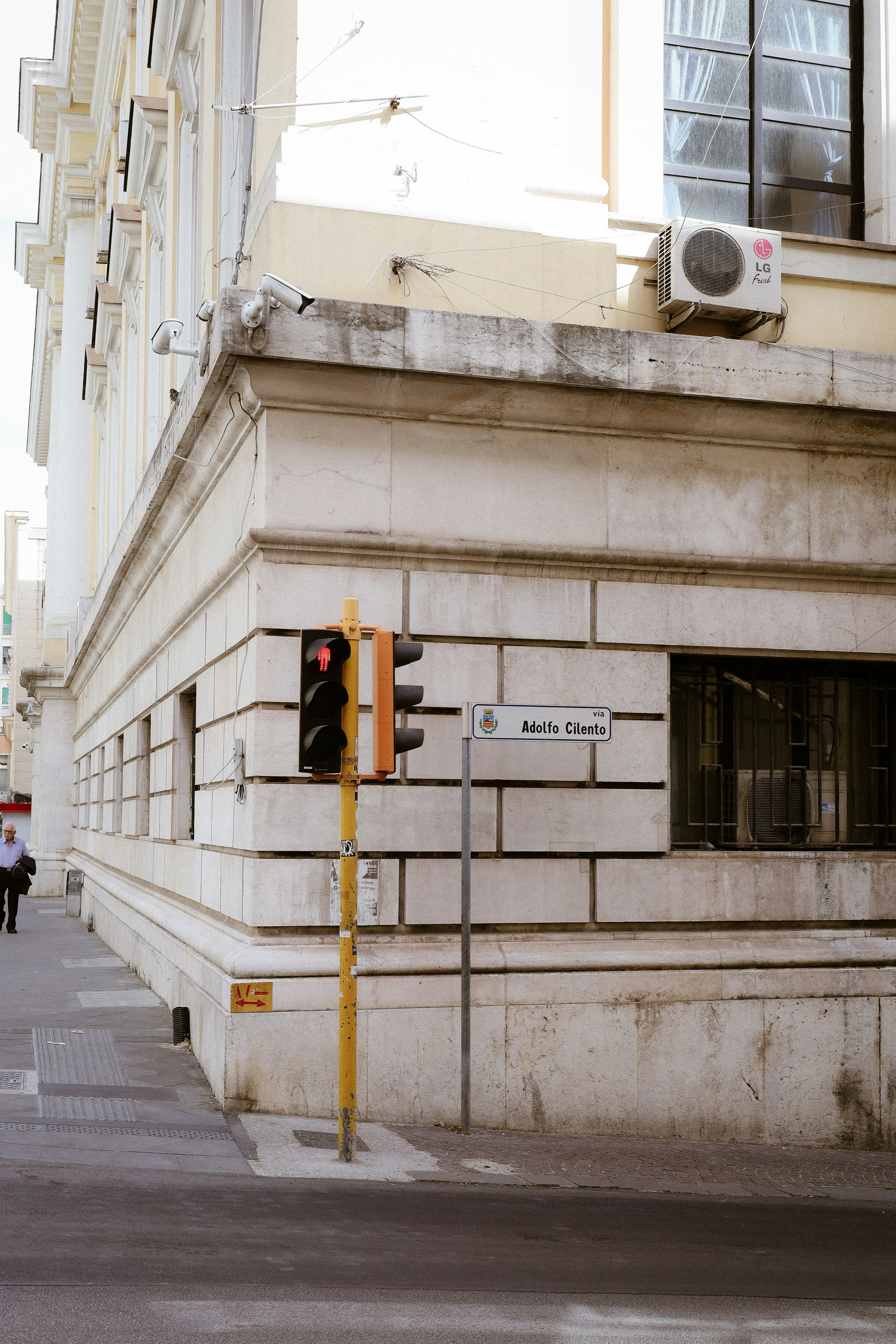 Traffic light displaying red at a city intersection, with a street sign for 'Adolfo Ciento' visible. The scene captures the essence of urban life.