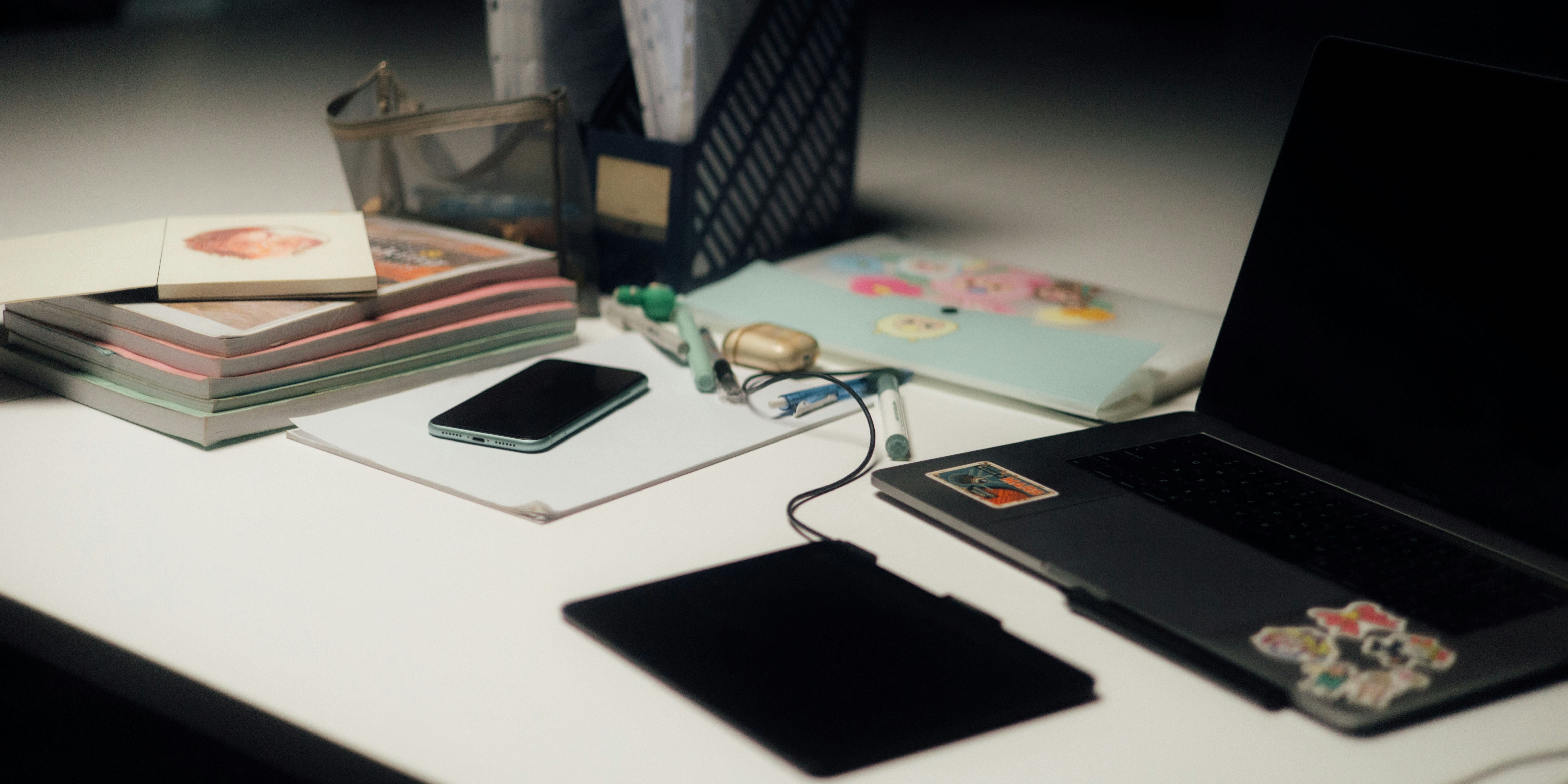 A cluttered desk featuring notebooks, a smartphone, and a laptop, showcasing a creative workspace filled with personal touches.