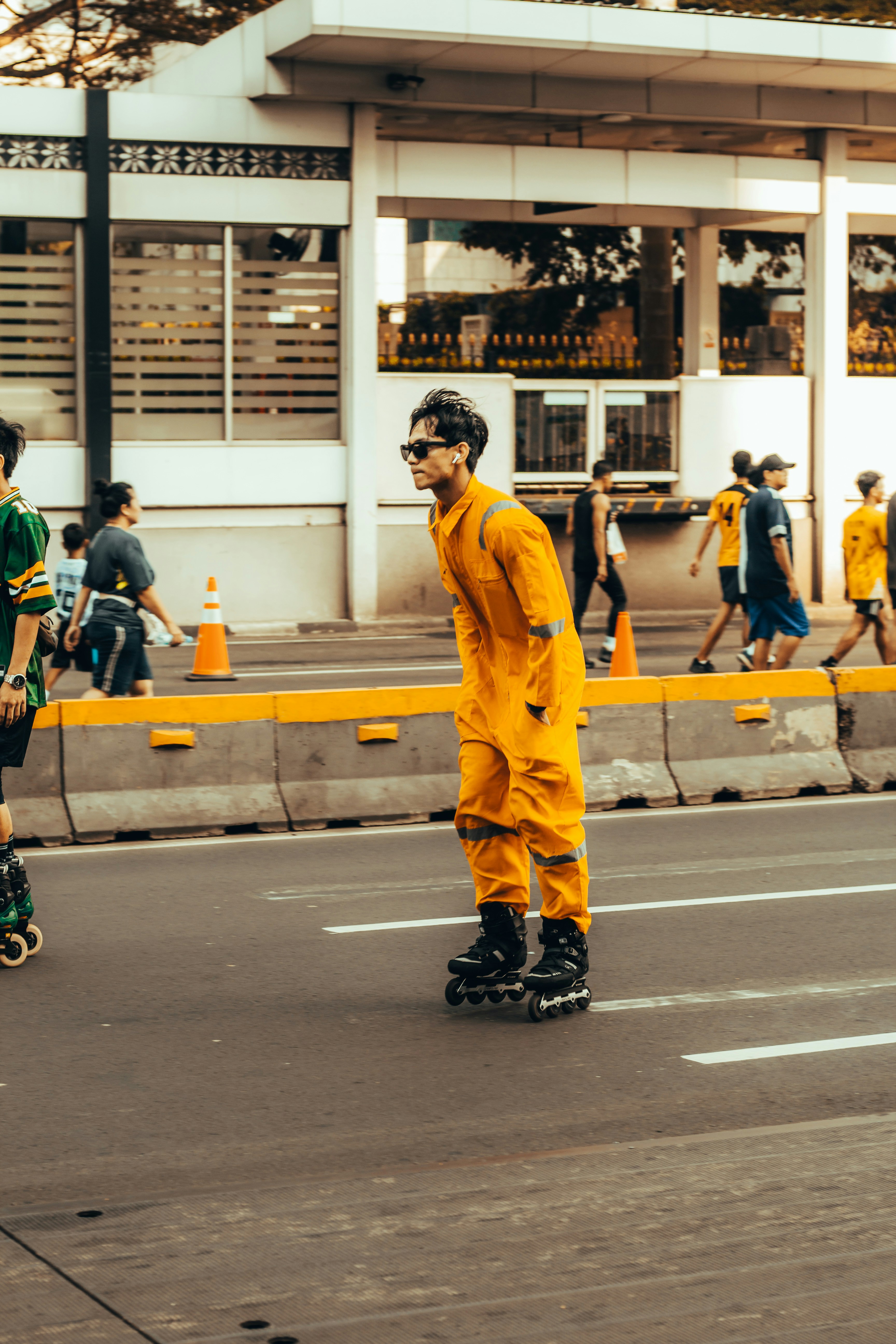 A rollerblader in a bright yellow jumpsuit glides through a city street, surrounded by pedestrians and traffic cones. The scene captures the energy and movement of urban life.