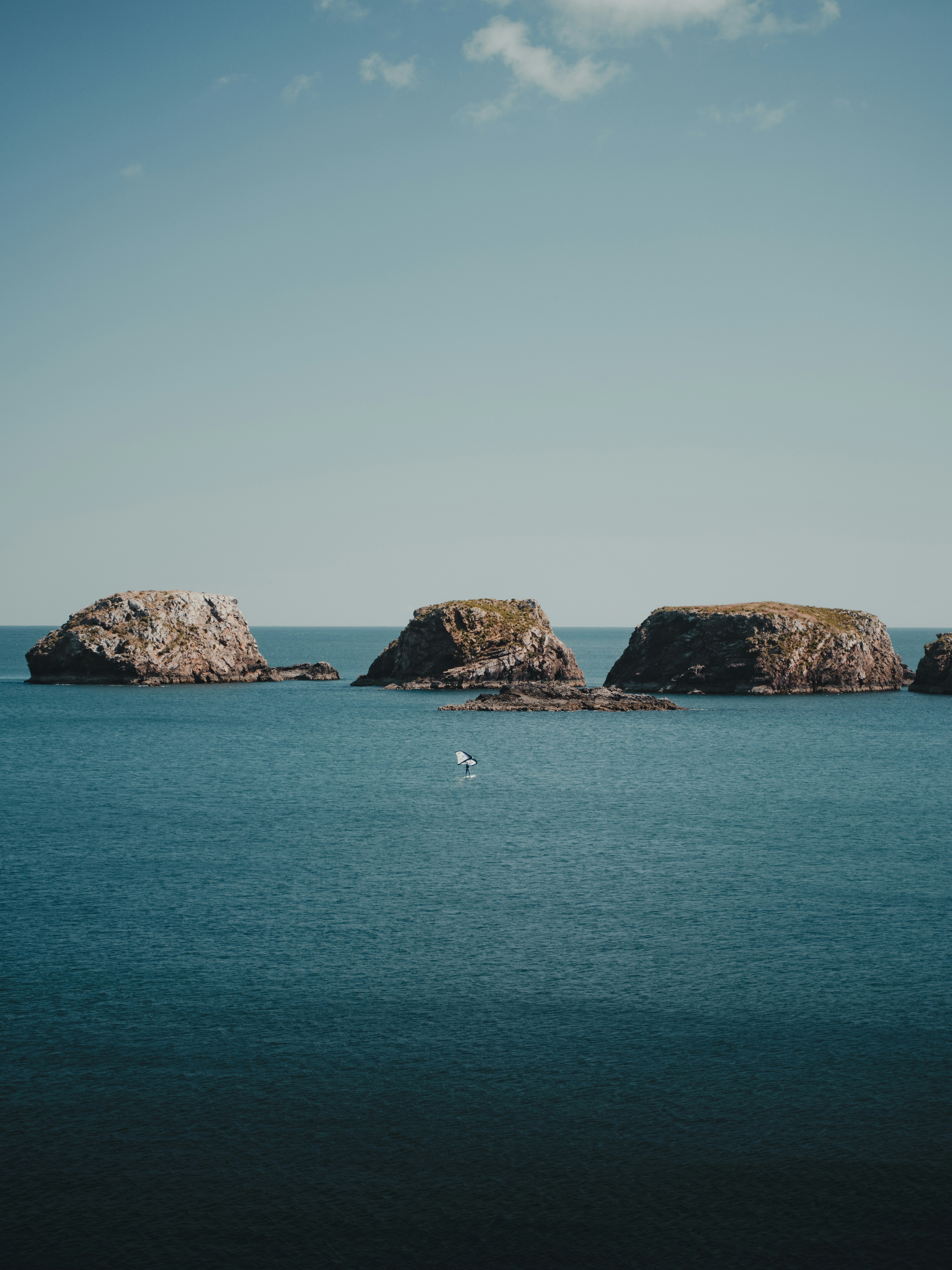 Rocks sit in the sea beneath a blue sky.