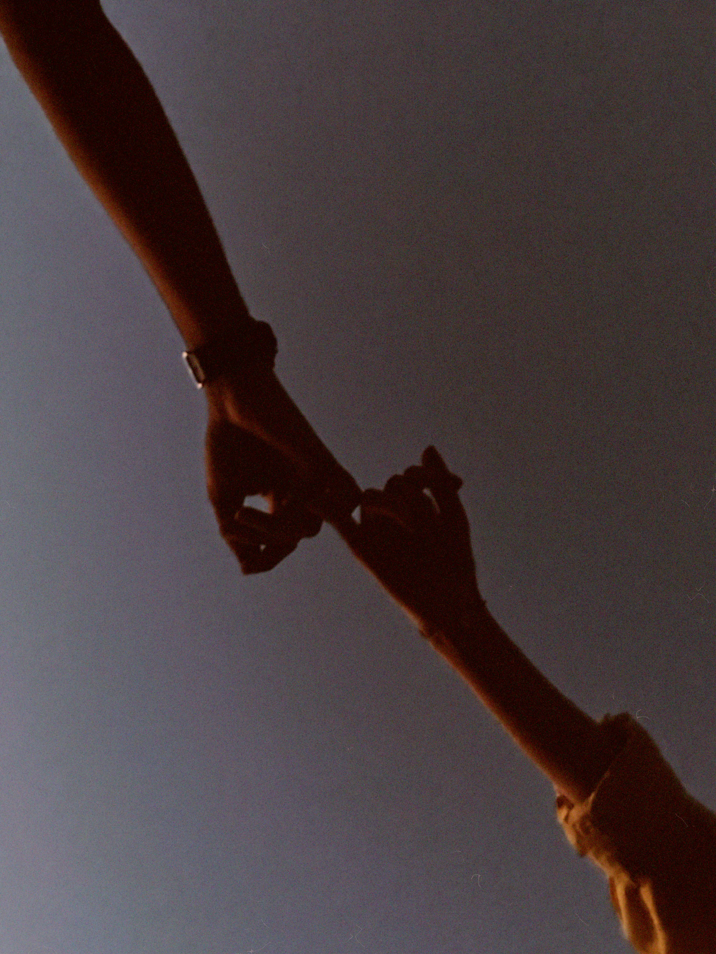 Hands clasping pinky fingers against a clear sky.