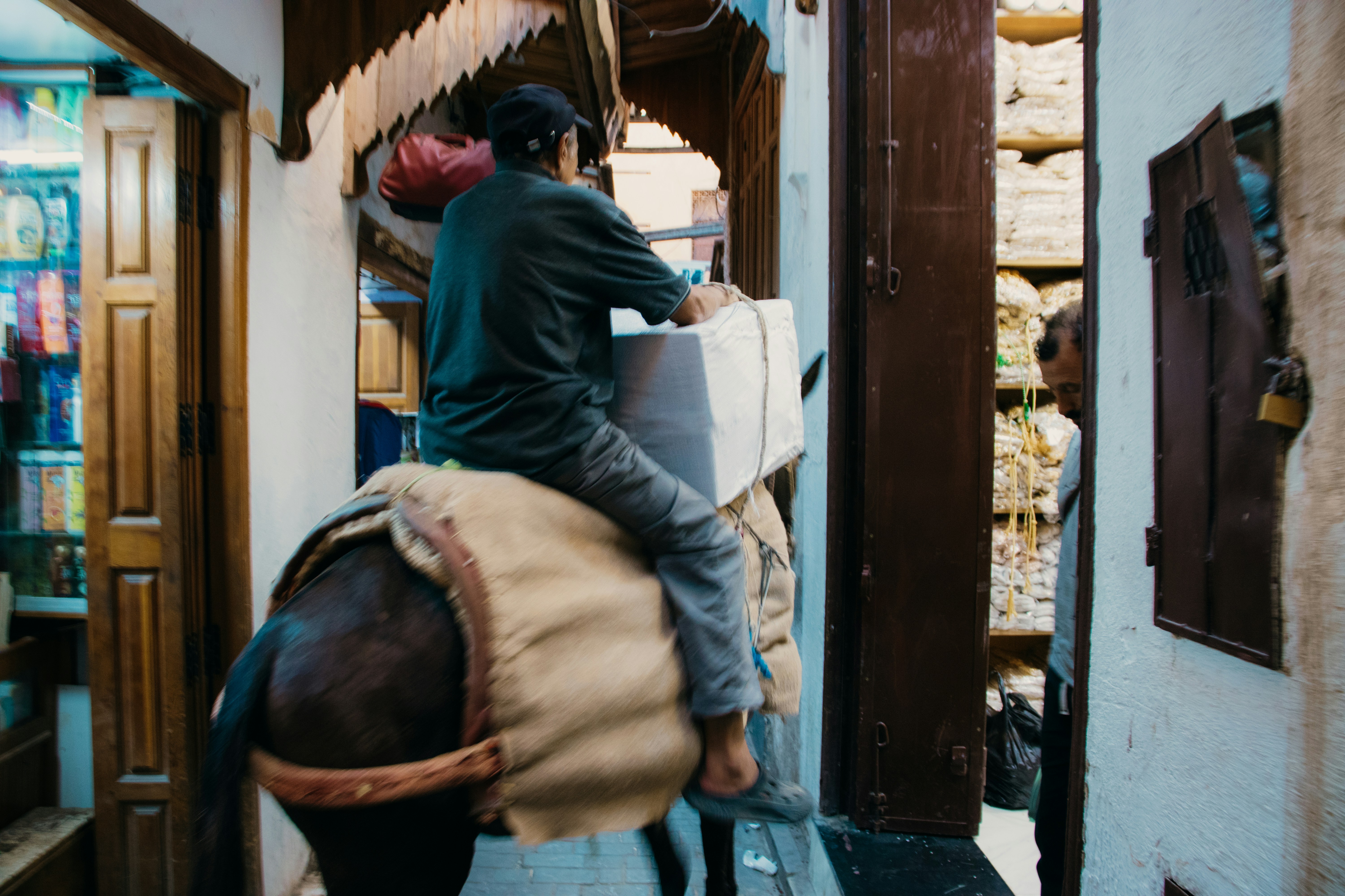 A man rides a donkey through a narrow street.