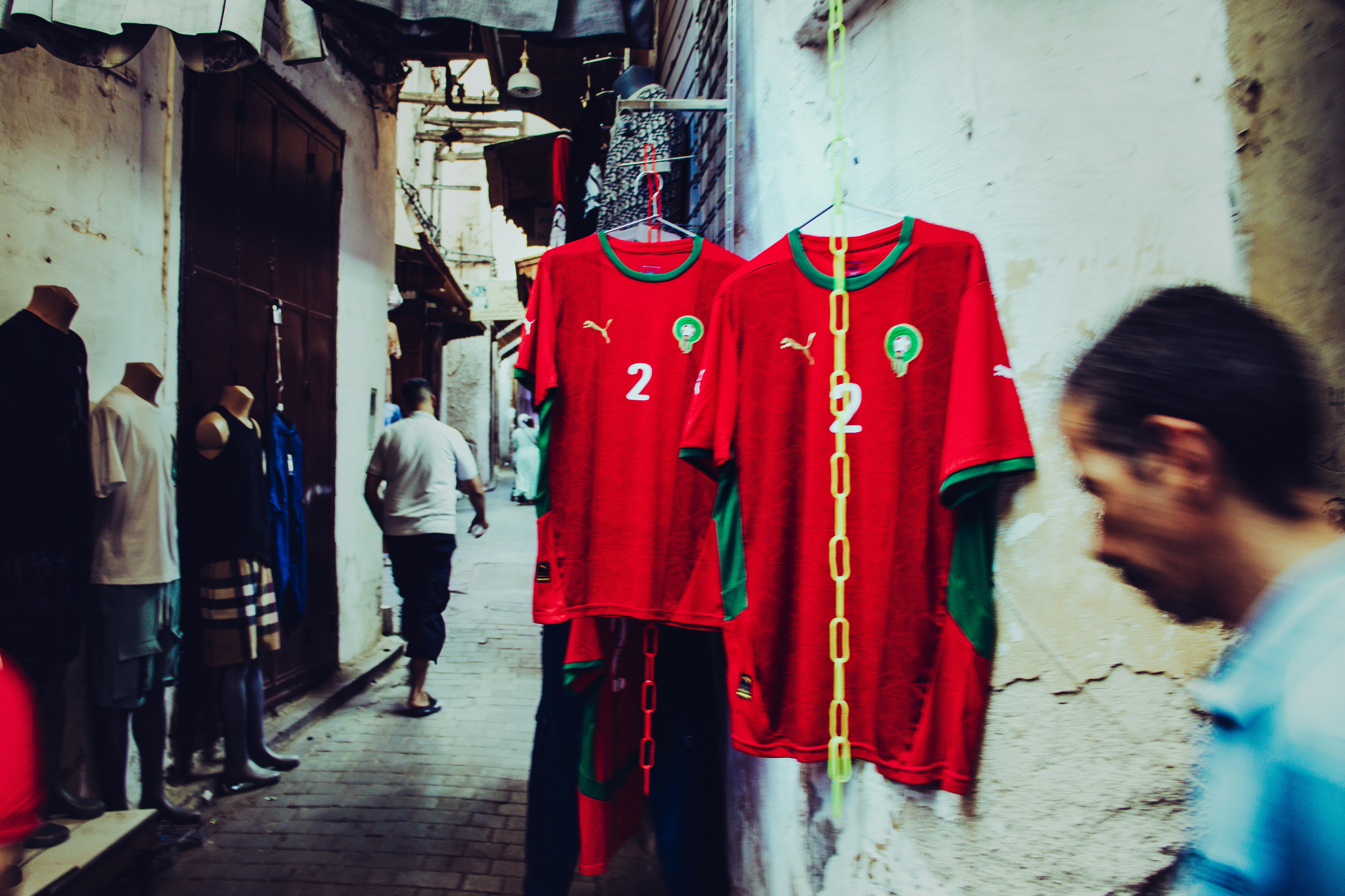 Moroccan soccer jerseys hang in a narrow street.