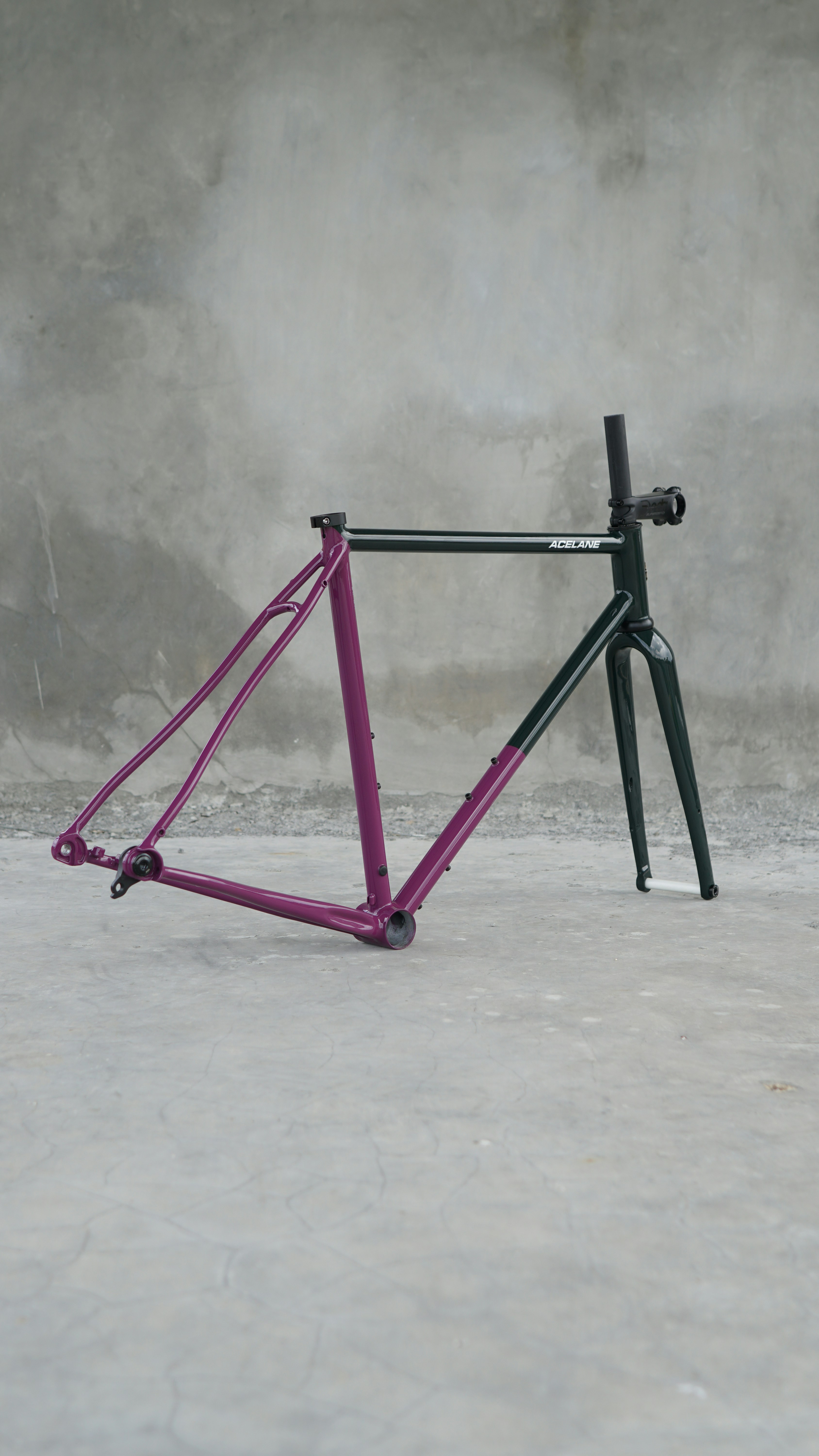 Vibrant bicycle frame showcasing a unique blend of purple and green colors against a minimalist concrete backdrop.