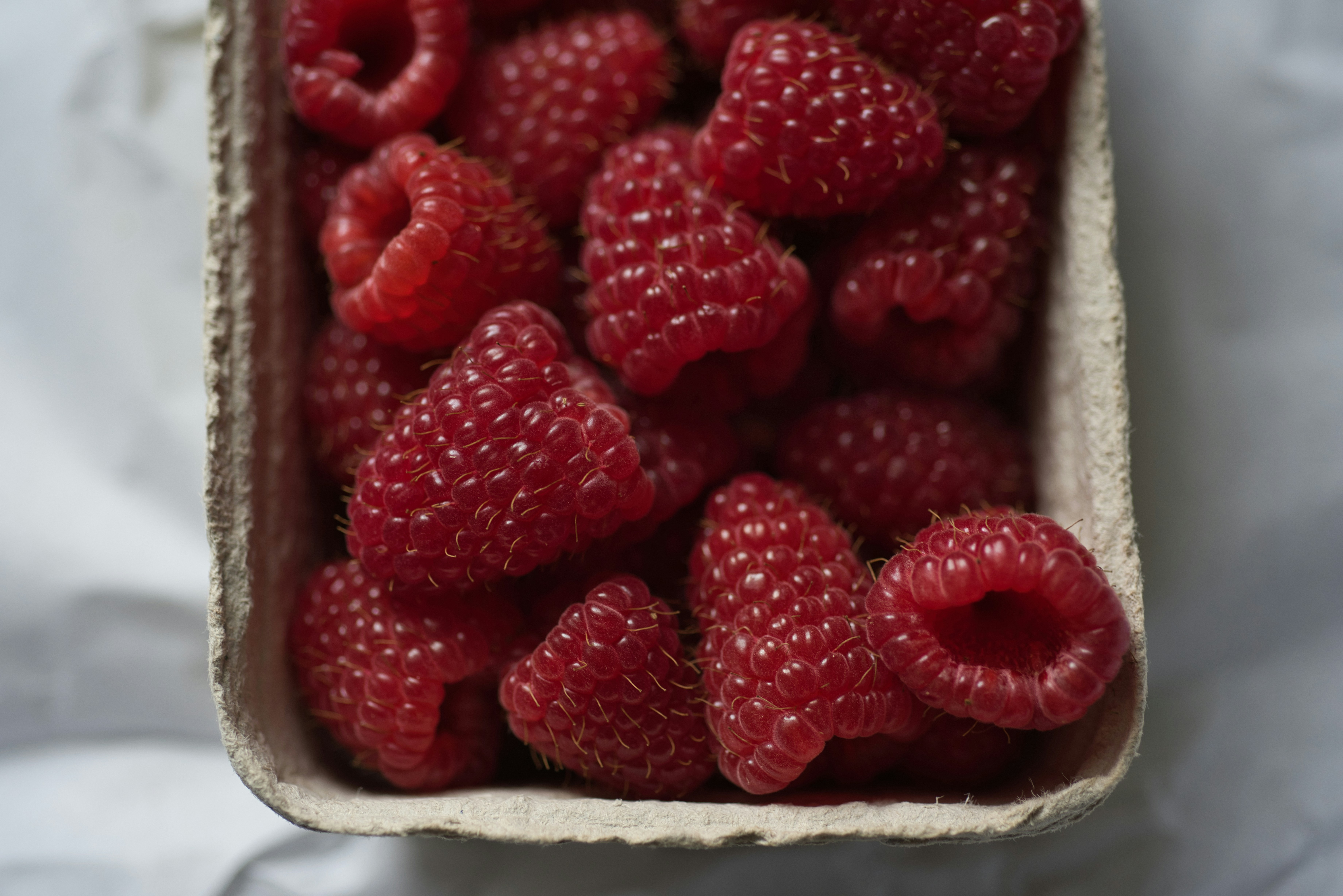 Fresh raspberries neatly packed in a small box. Sweet summer raspberries arranged in a rustic container. | A box full of fresh, red raspberries.