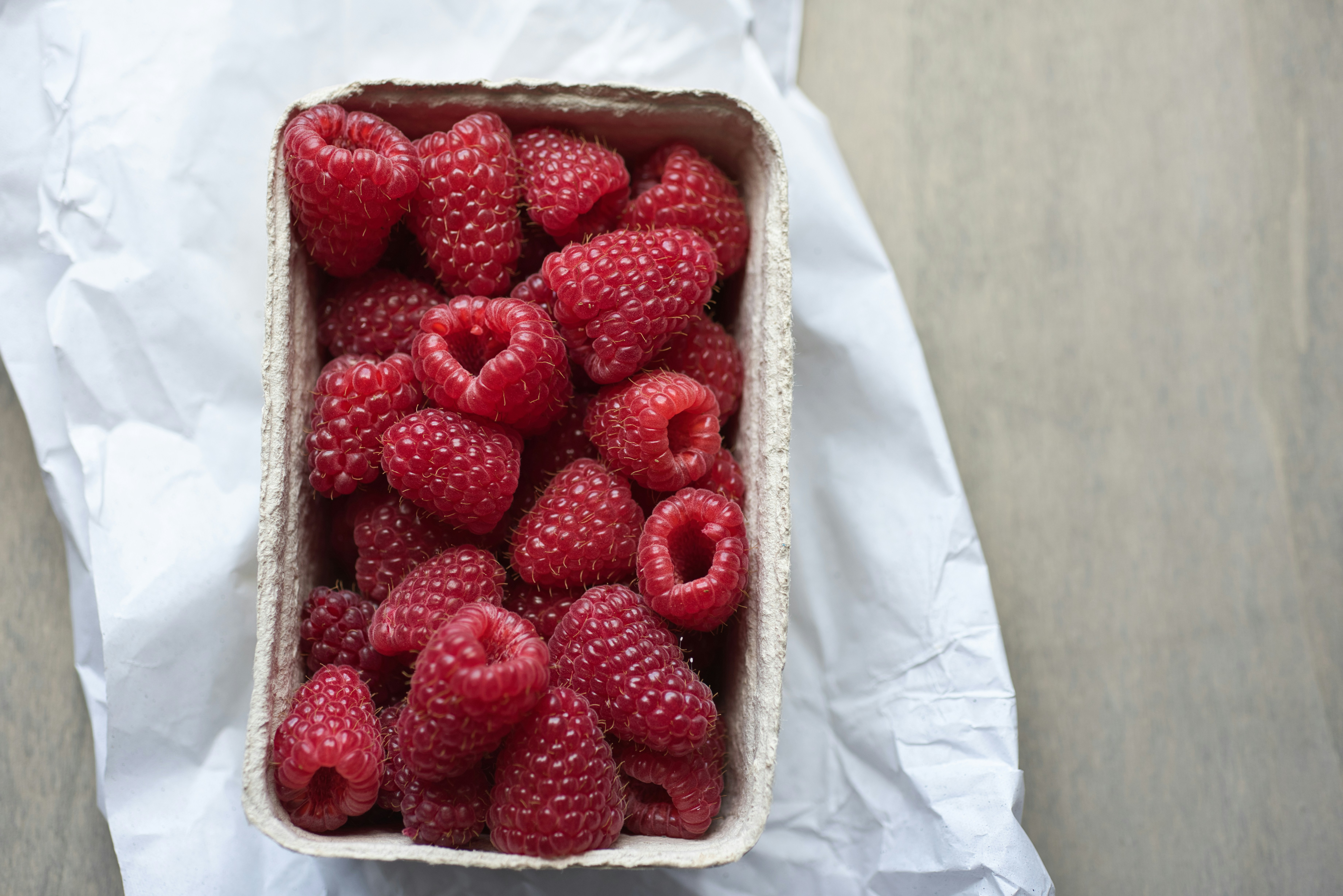 A basket filled with fresh, plump raspberries resting on crumpled white paper.