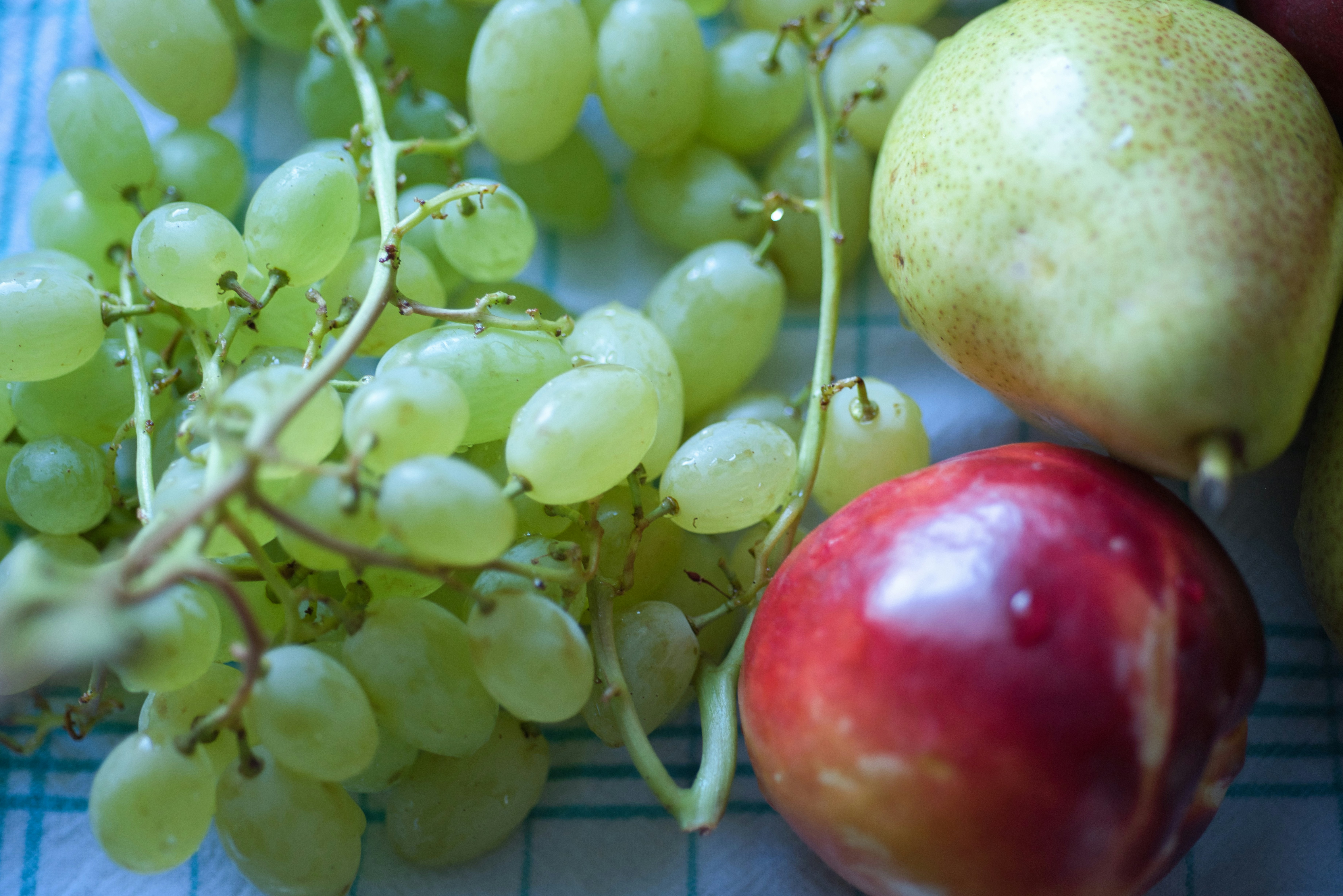 Fresh seasonal fruits placed on a clean dishcloth. A vibrant fruit arrangement on a textured tea towel. Natural still life with mixed fruits on cotton fabric. | Grapes, apple, and pears in close-up view.