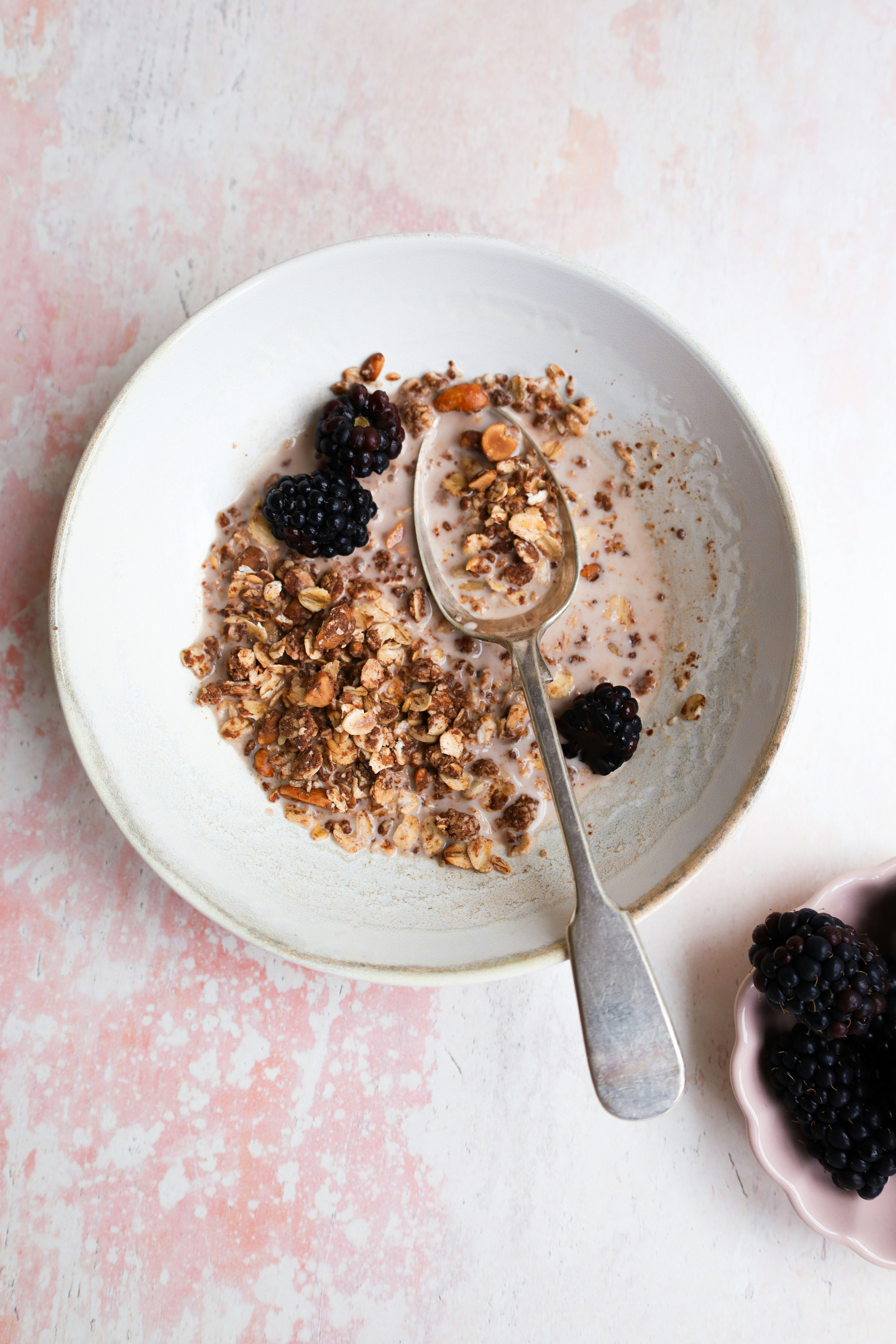 A bowl of homemade Granola with black berries on a pink backdrop | Granola with berries in a bowl, ready to eat.