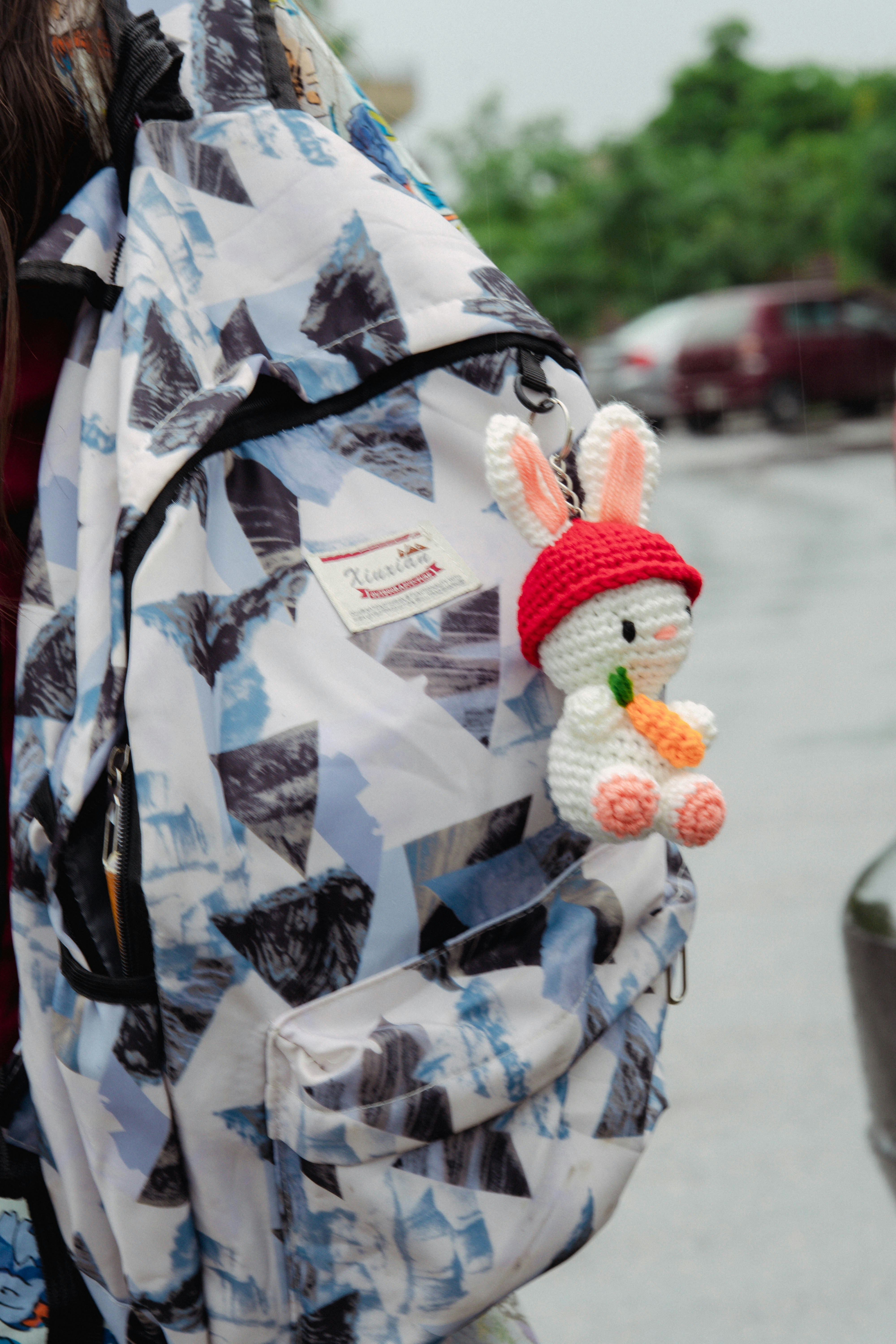 A handmade crochet bunny styled with a bright red hat and a tiny bag, posed in natural light for product photography. This whimsical and cozy creation is perfect for showcasing the charm of slow craft, eco-friendly toys, and character-rich handmade decor. Ideal for nursery inspiration, gift ideas, and artisan showcases. | A backpack with a crochet bunny is shown.