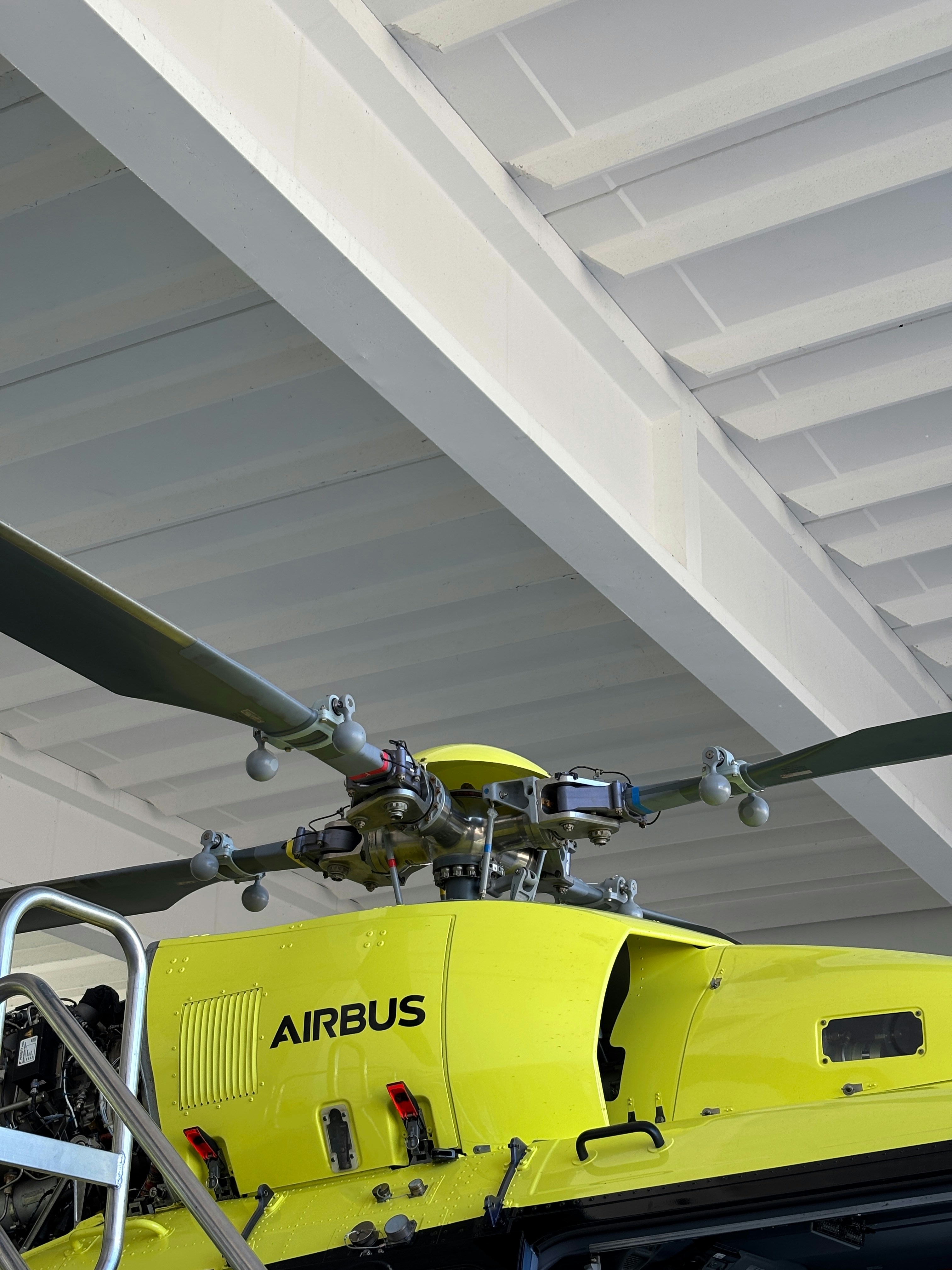 Sunlit Yellow Airbus Helicopter Resting Beneath a White Hangar Truss