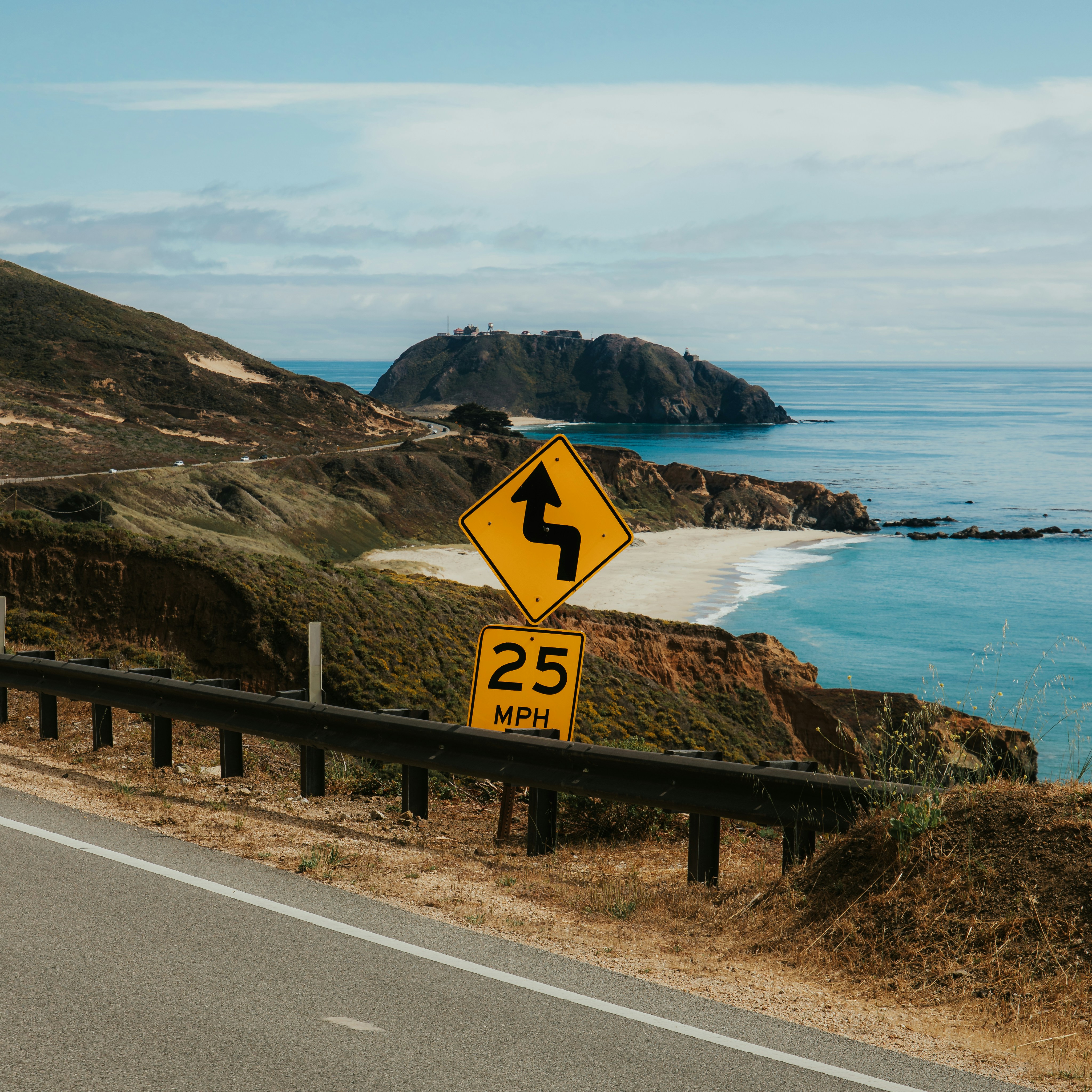 Winding road sign along a scenic coastal view.