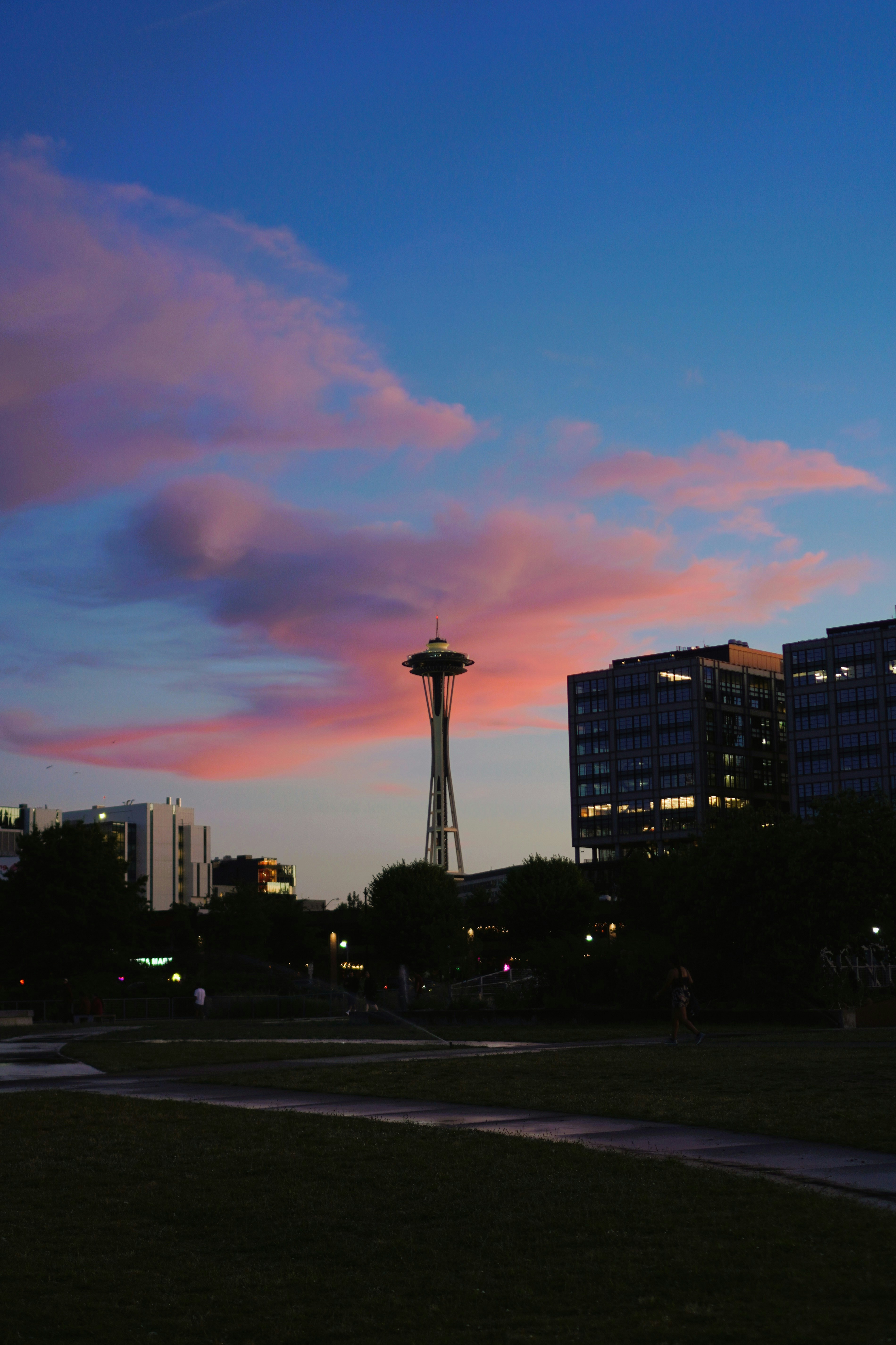 The Space Needle stands tall against a gradient sky, adorned with soft pink clouds as evening descends over the cityscape.