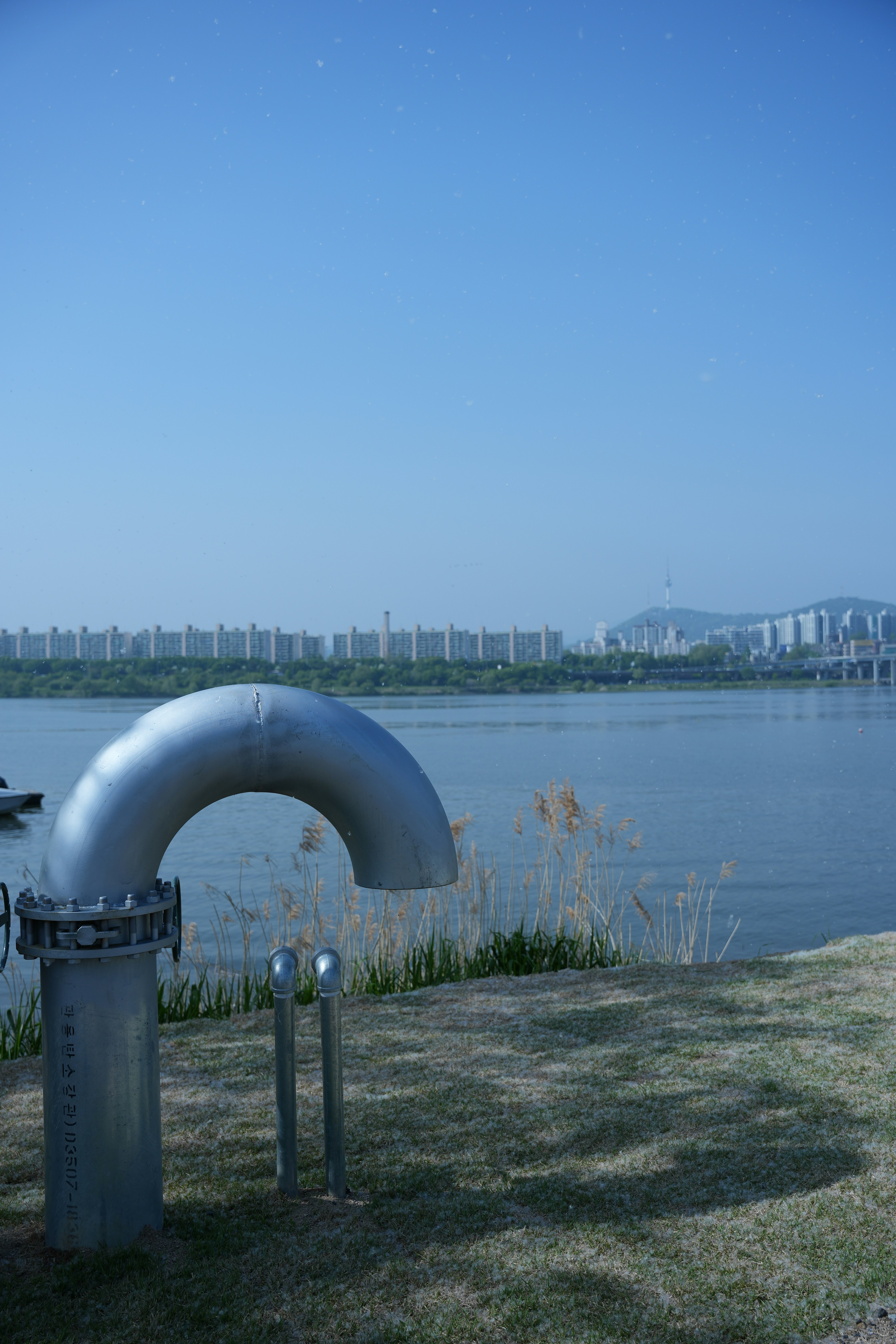 A metal pipe stands near a river.