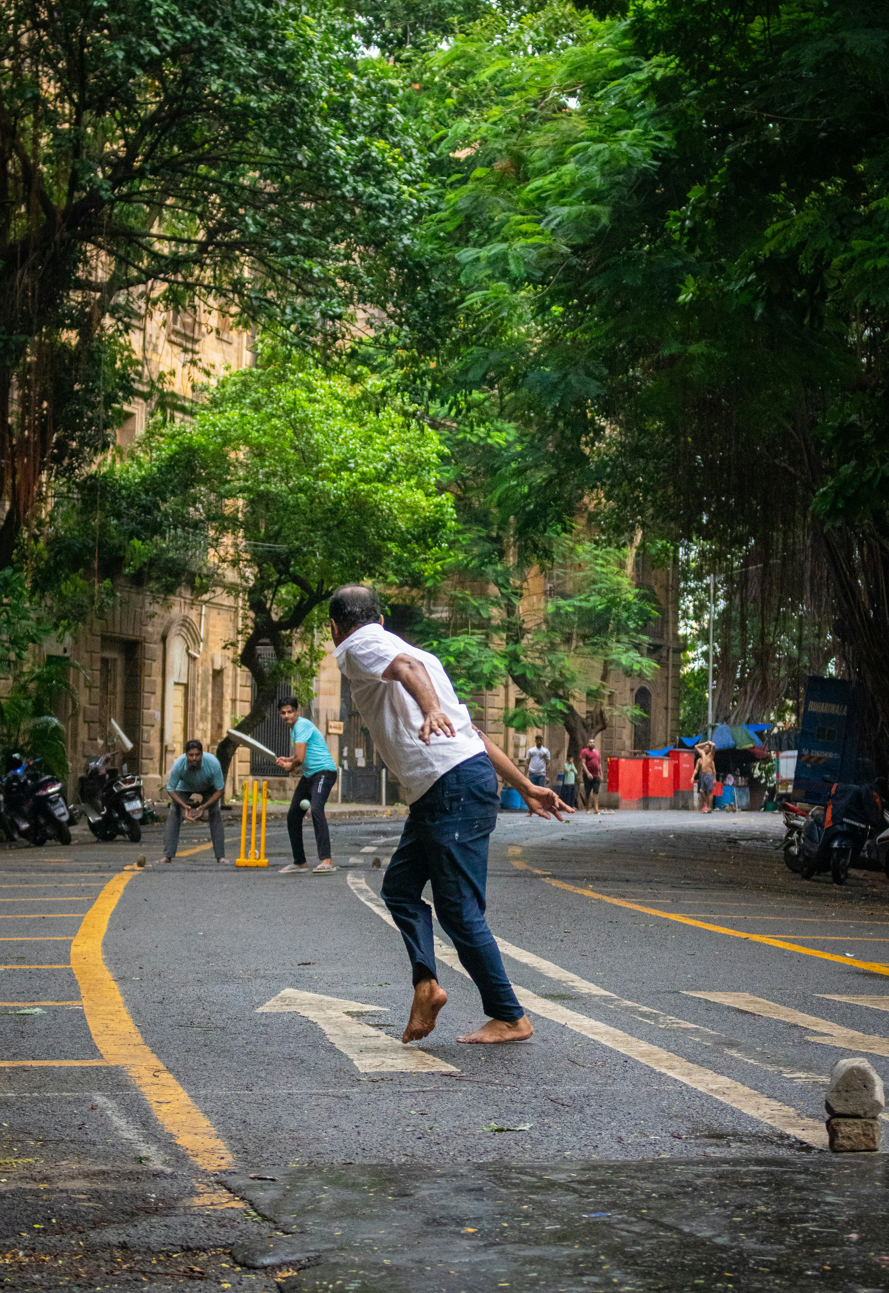 People play street cricket (gully cricket) on the streets of Ballard Estate, Fort, Mumbai on a Sunday afternoon. | People play cricket in the street.