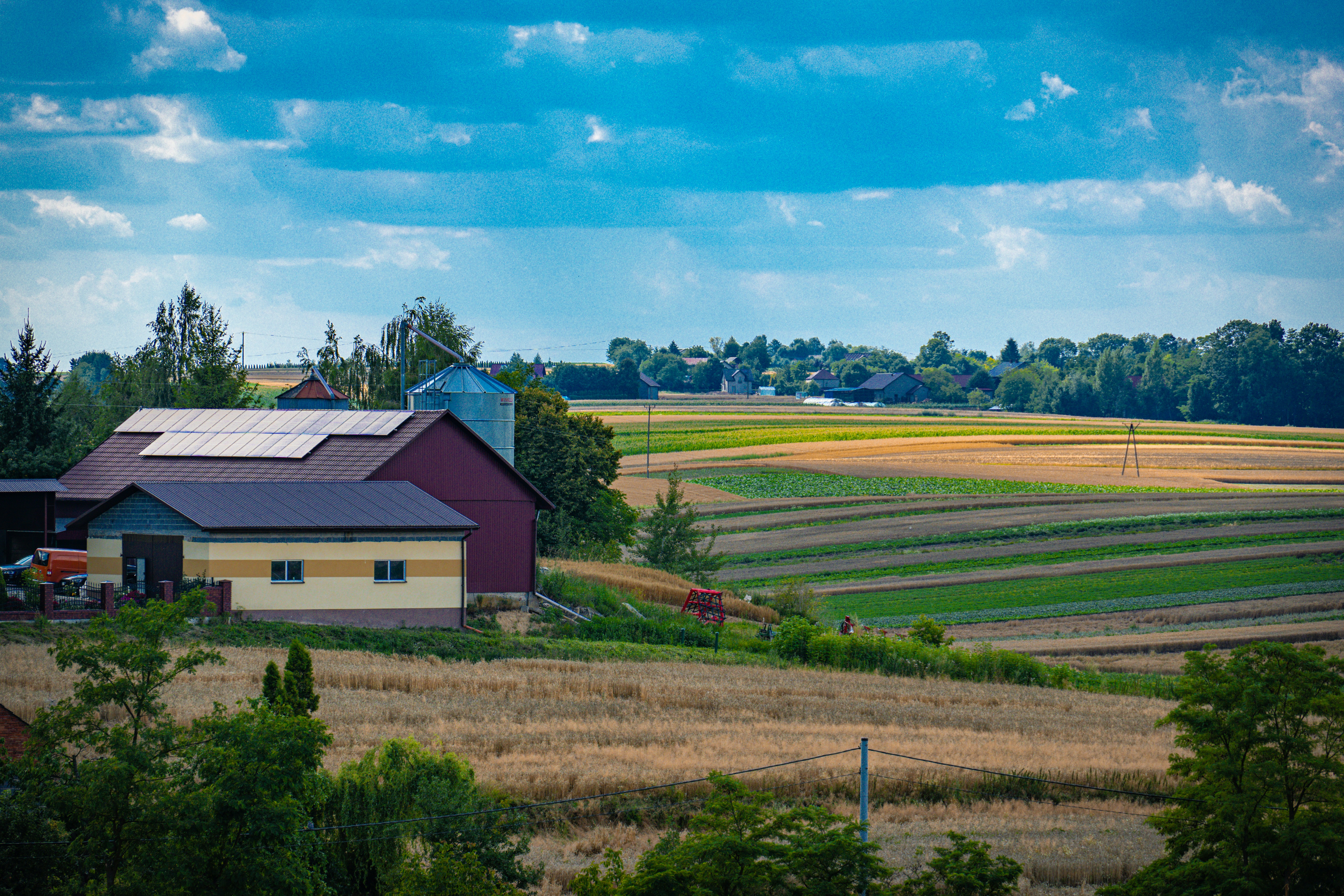 Farm buildings sit among fields under a blue sky.