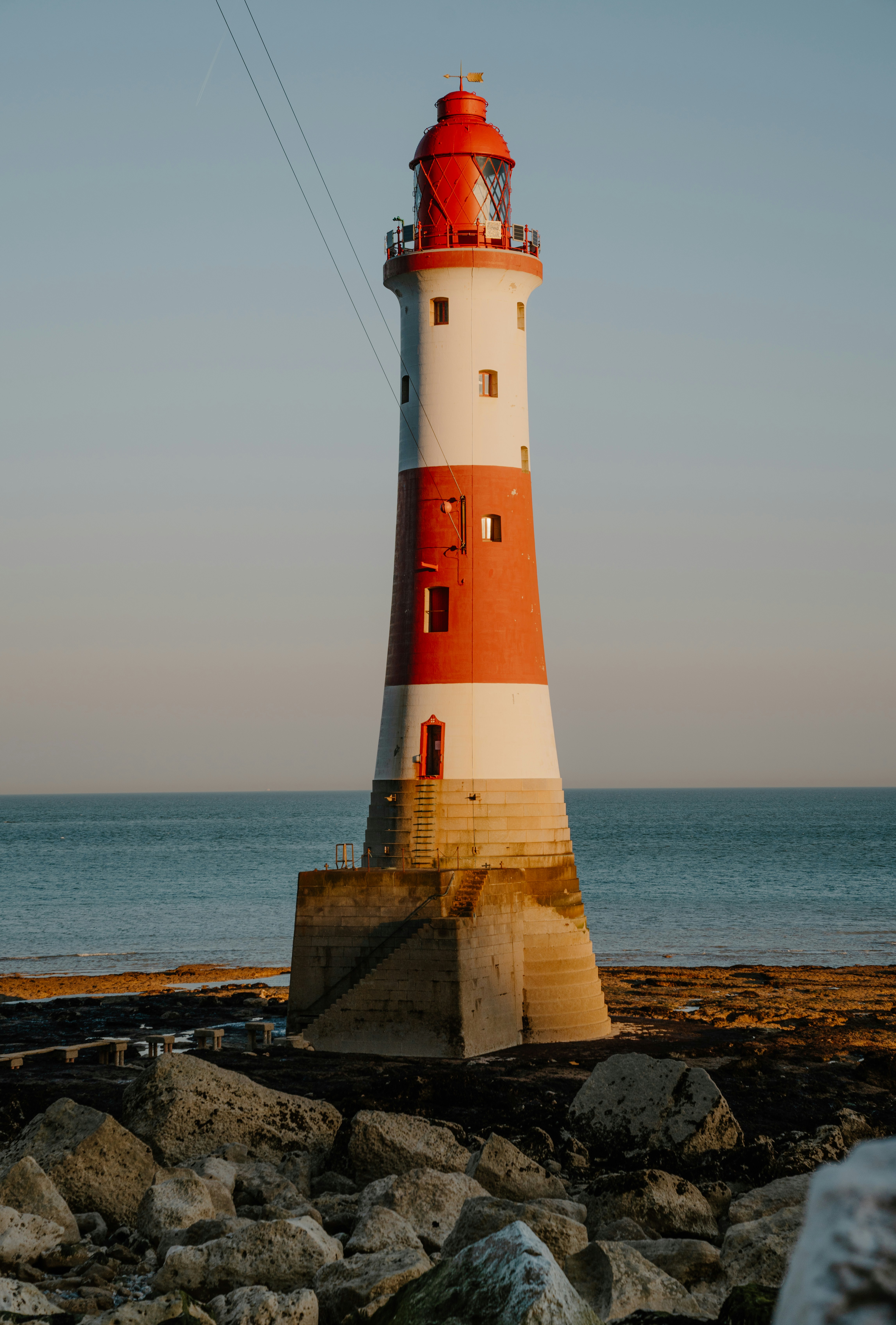 Famous Beachy Head Lighthouse in the South Downs National Park at dusk. | A lighthouse stands tall against the sea.