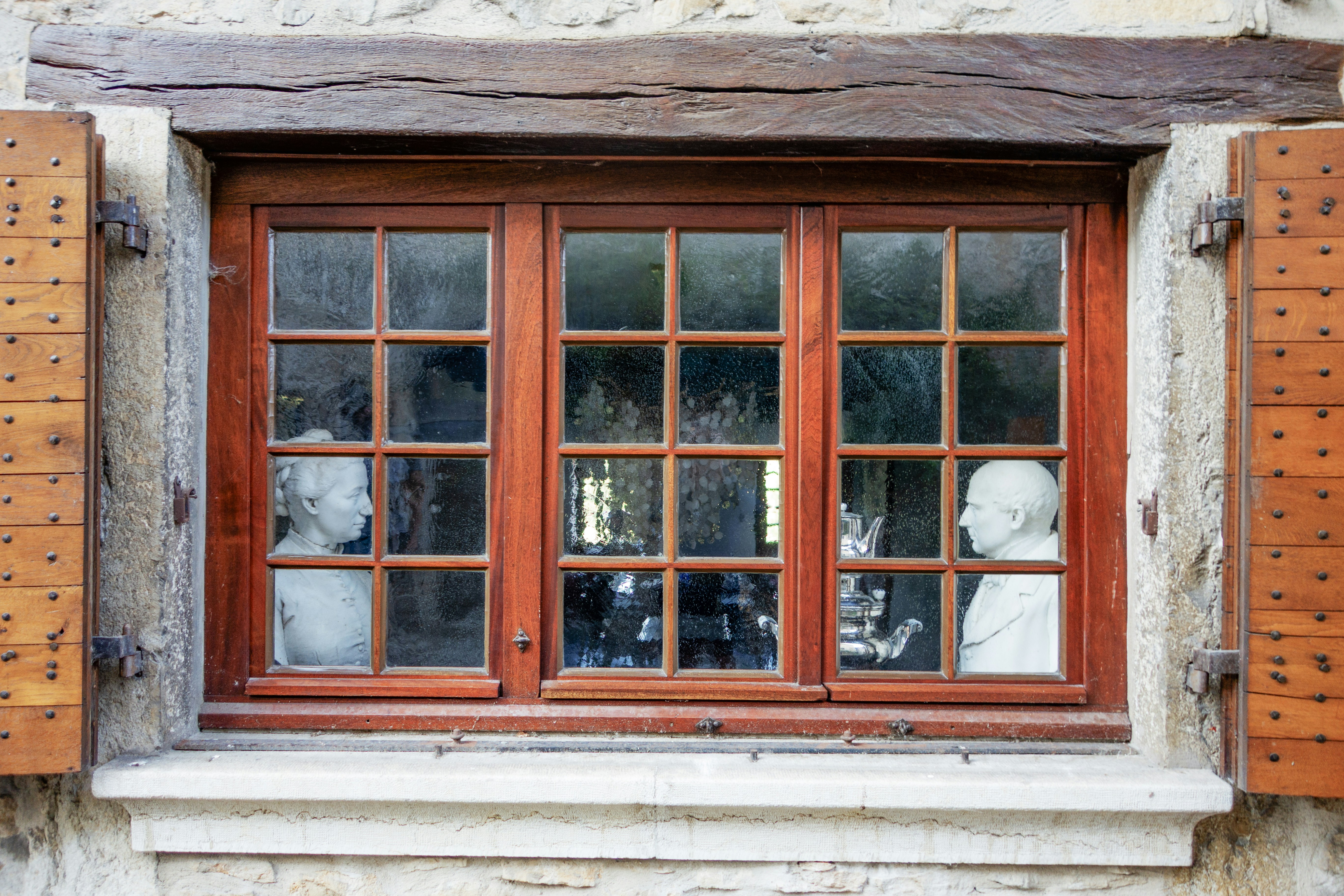Two busts flank a window in a stone building.