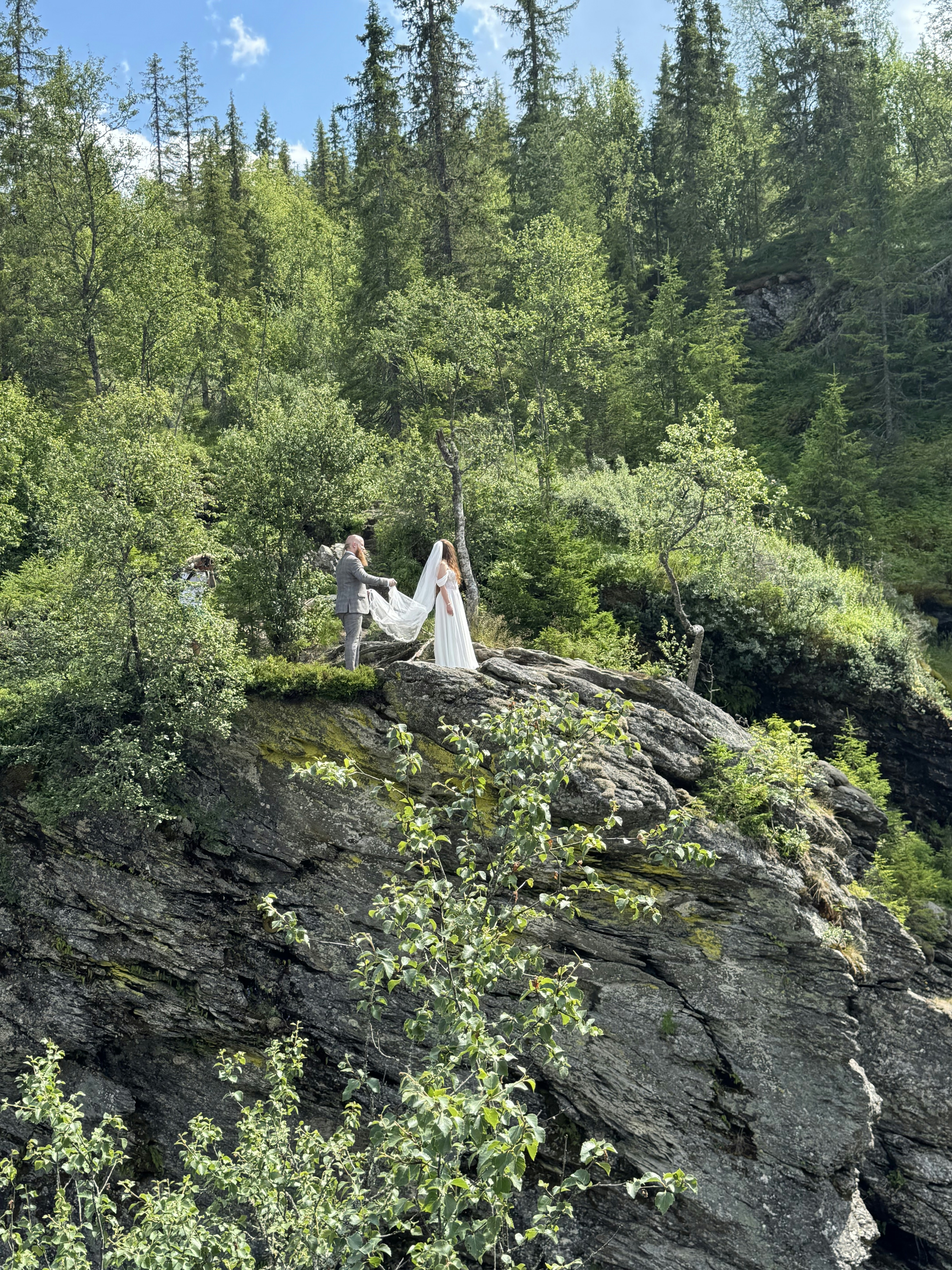 Bride and groom standing on a rocky outcrop surrounded by lush greenery, capturing a serene wedding moment.