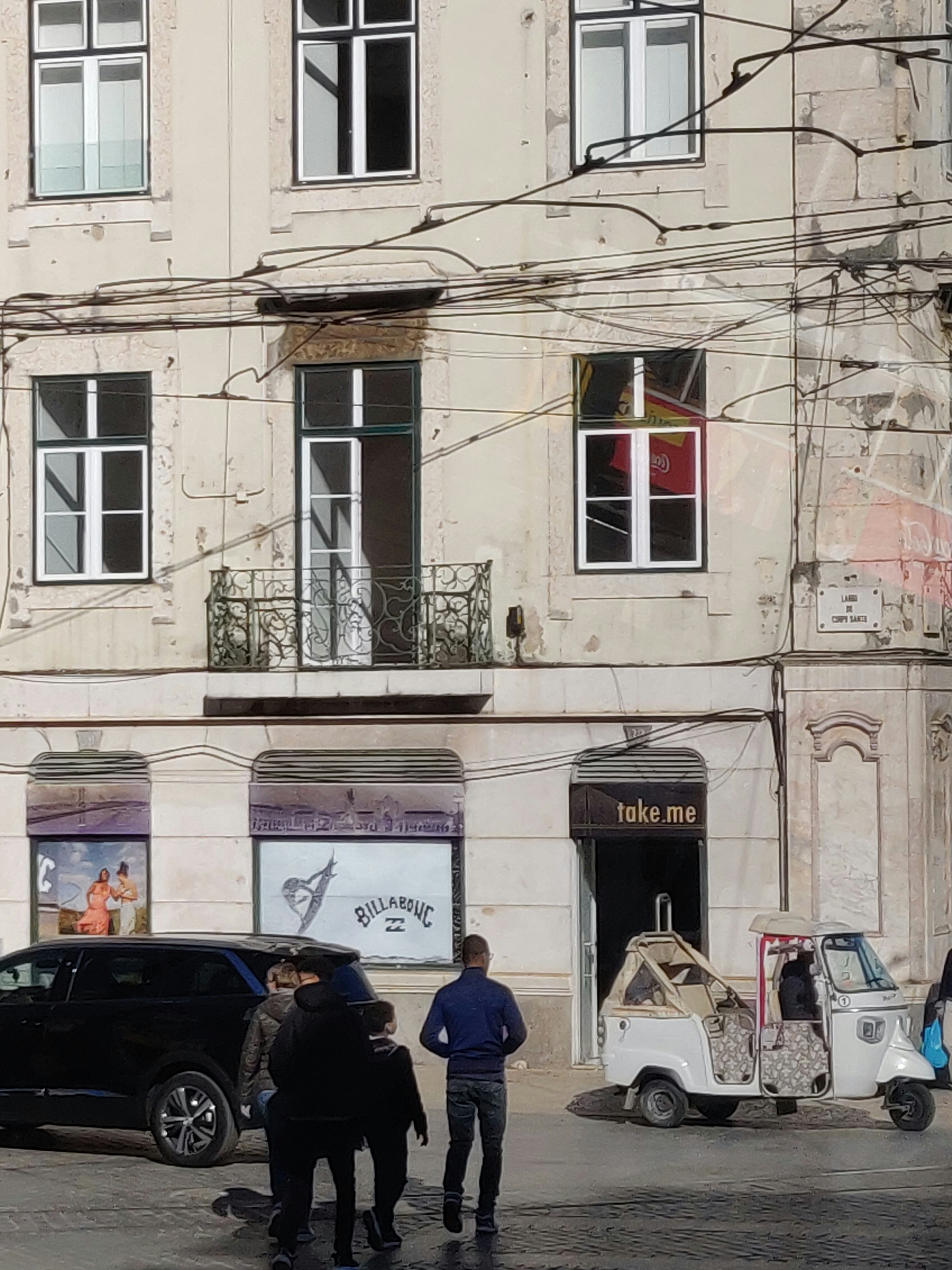 A historic building adorned with intricate balcony ironwork, surrounded by bustling pedestrians and urban life. The scene captures the essence of city dynamics.