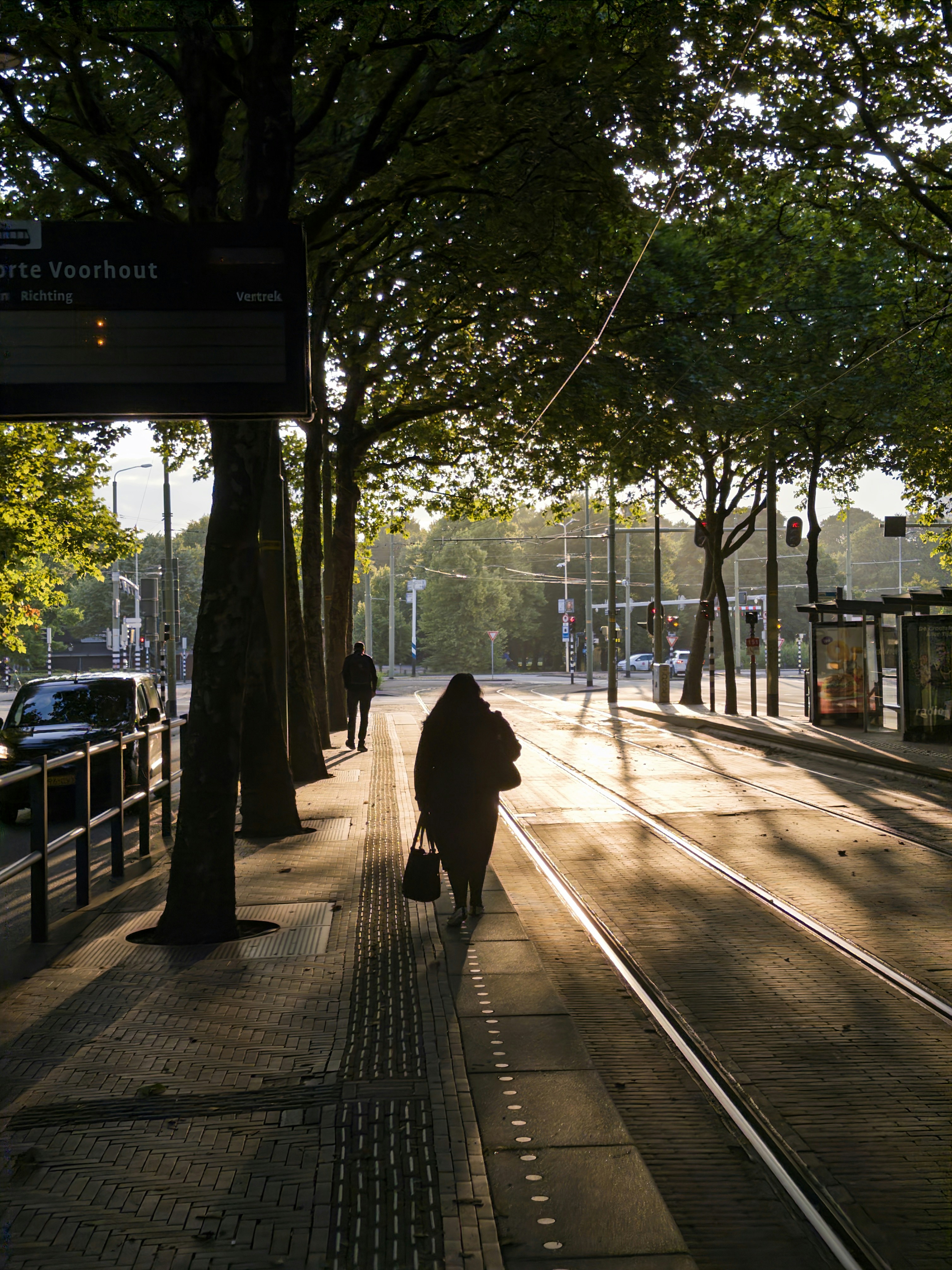 A person walks along a sunlit tram track.