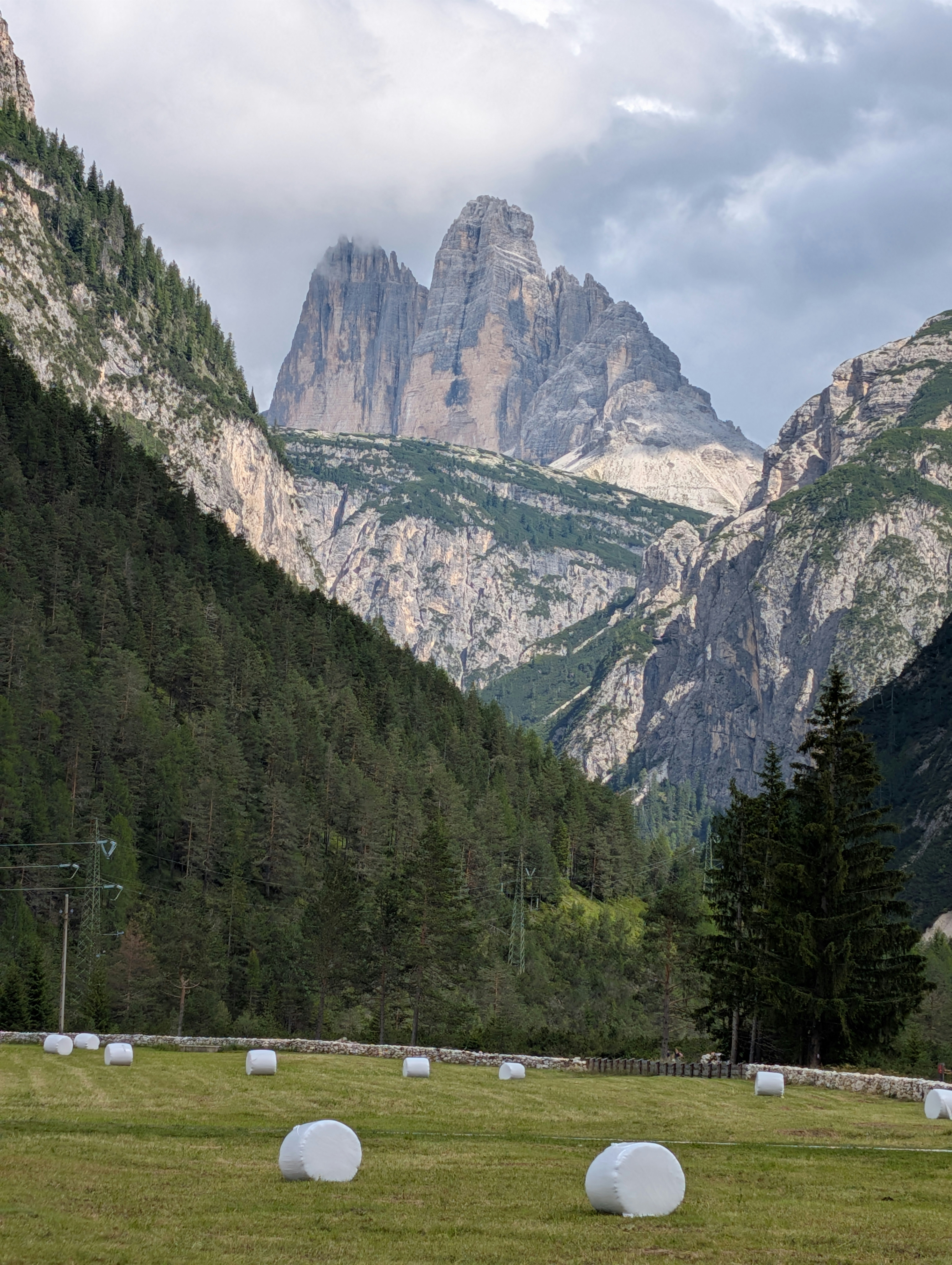Dramatic mountain range framed by lush greenery, with rolling clouds casting shadows on the rocky surfaces.