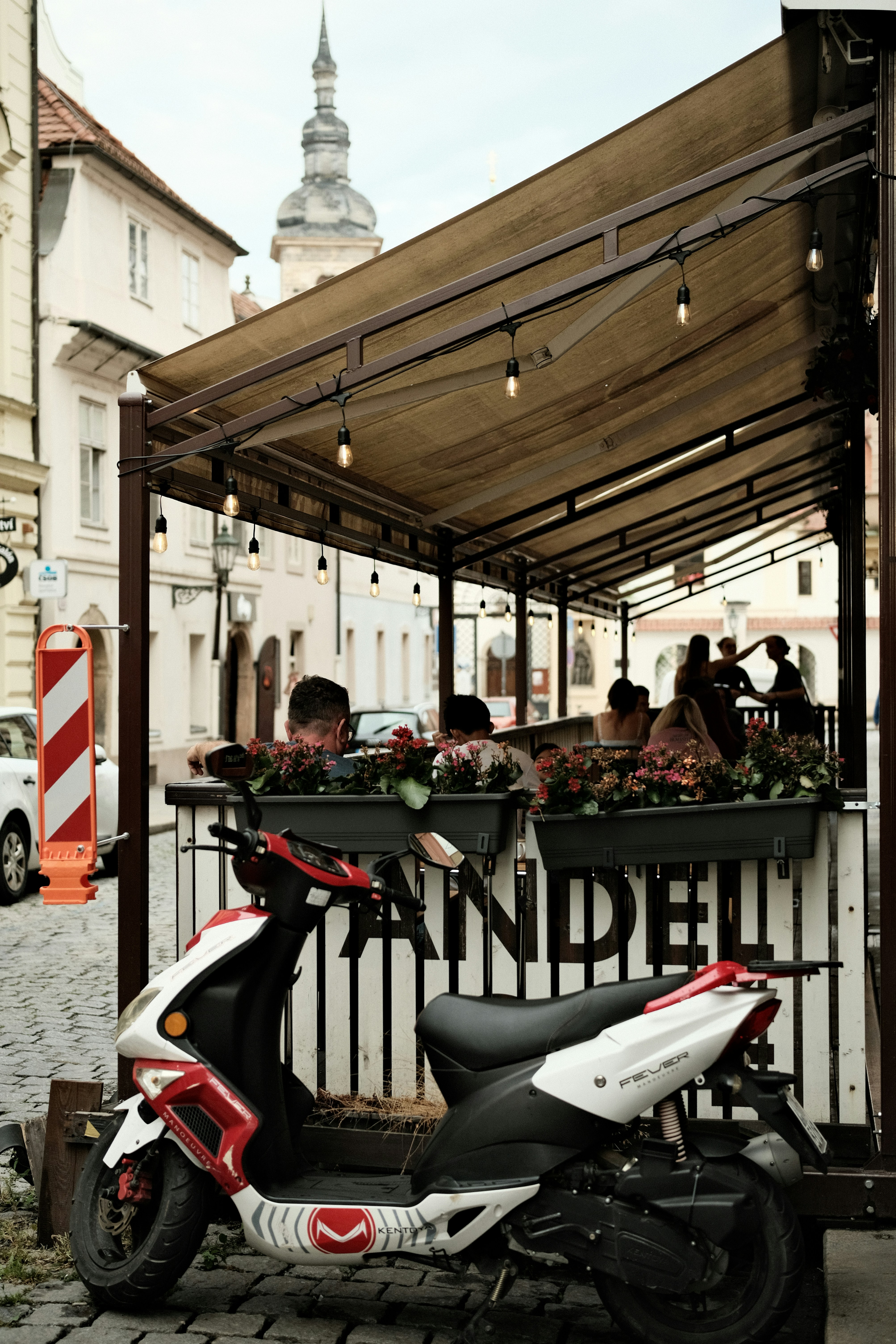Outdoor dining area with scooter in front. Andel means angel in Czech. | A scooter parked outside a restaurant.