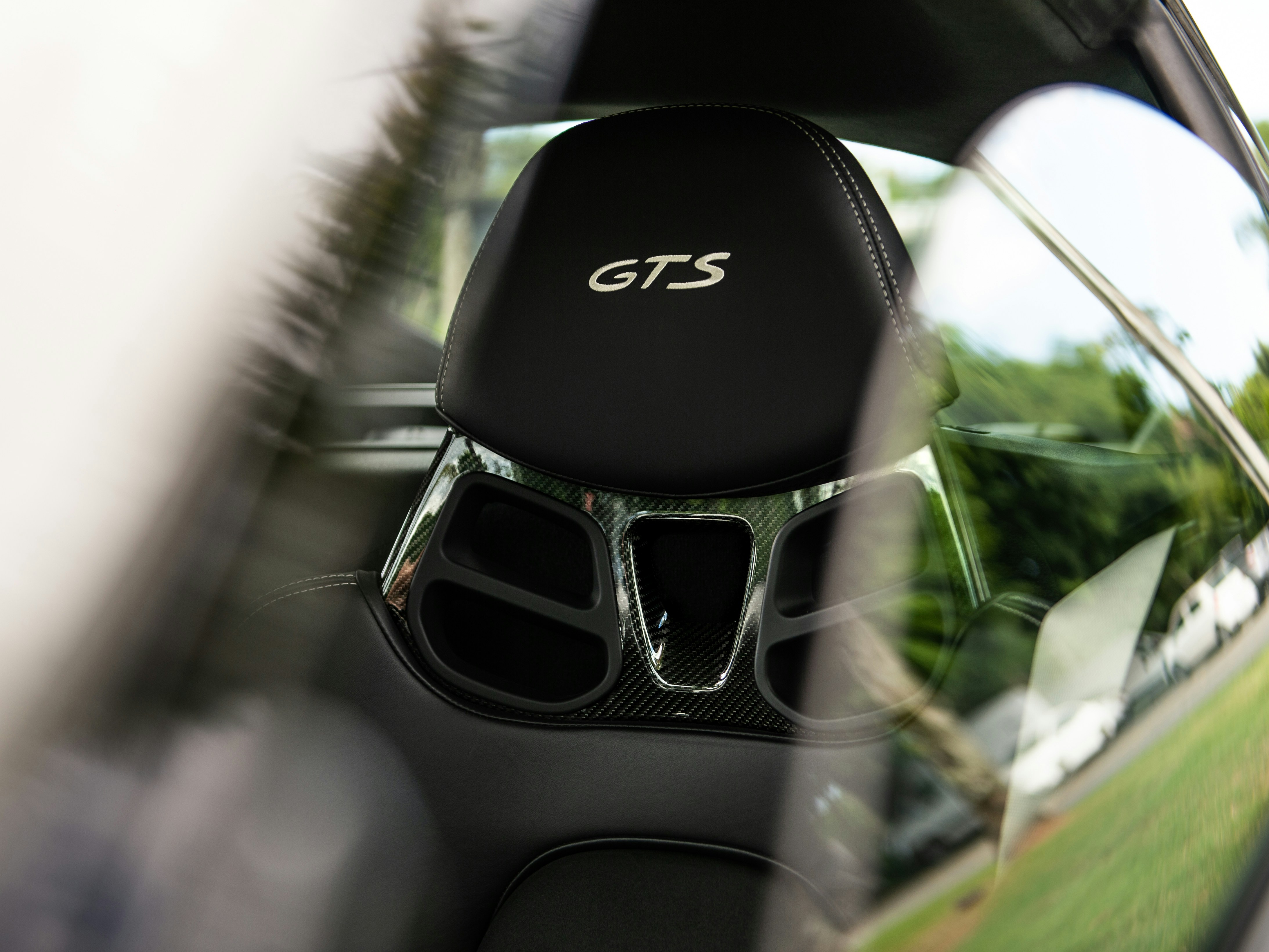 Interior view of a luxury car featuring a sleek GTS seat design with carbon fiber accents. The reflection adds depth to the composition.