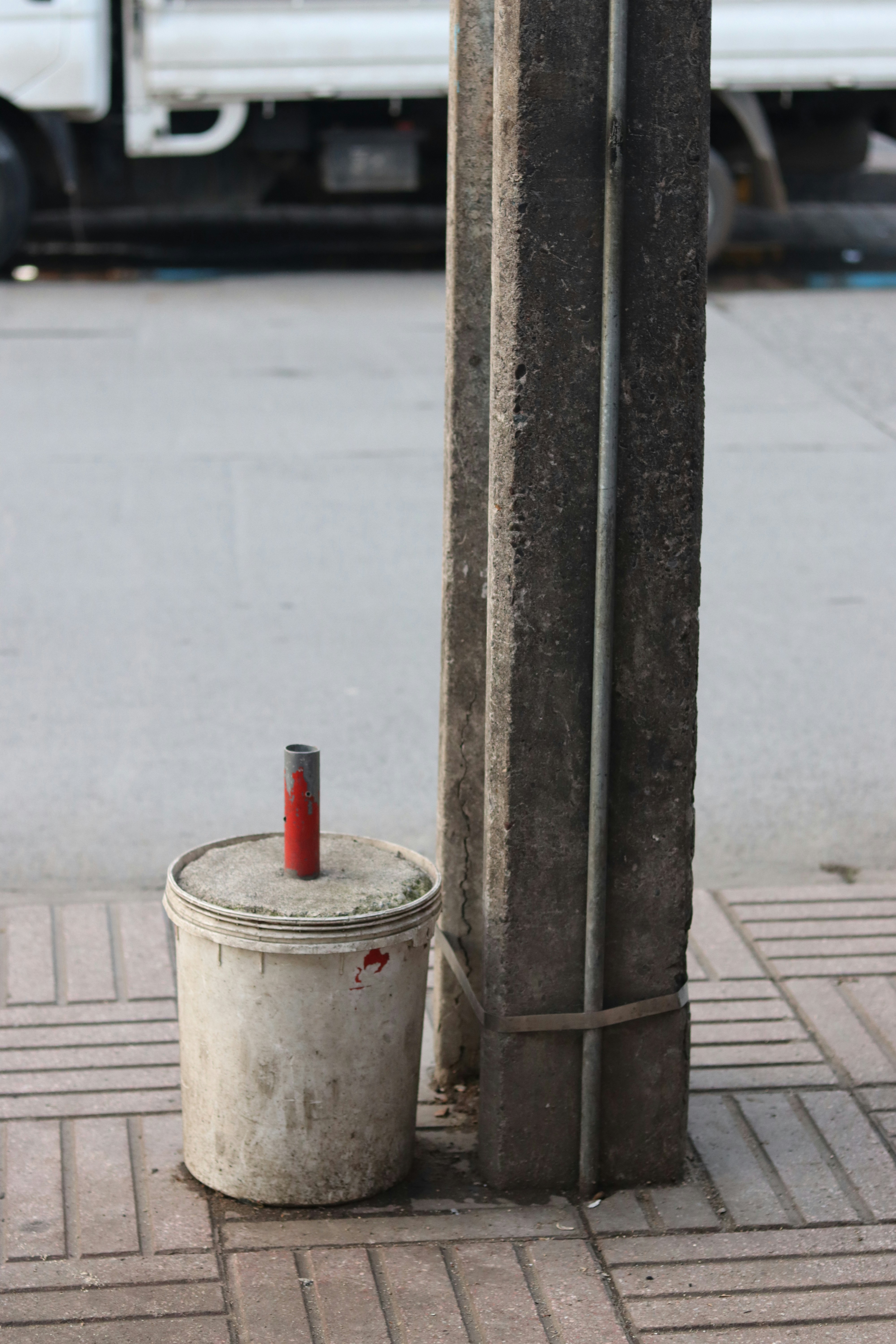 A trash can and a concrete post on the sidewalk.