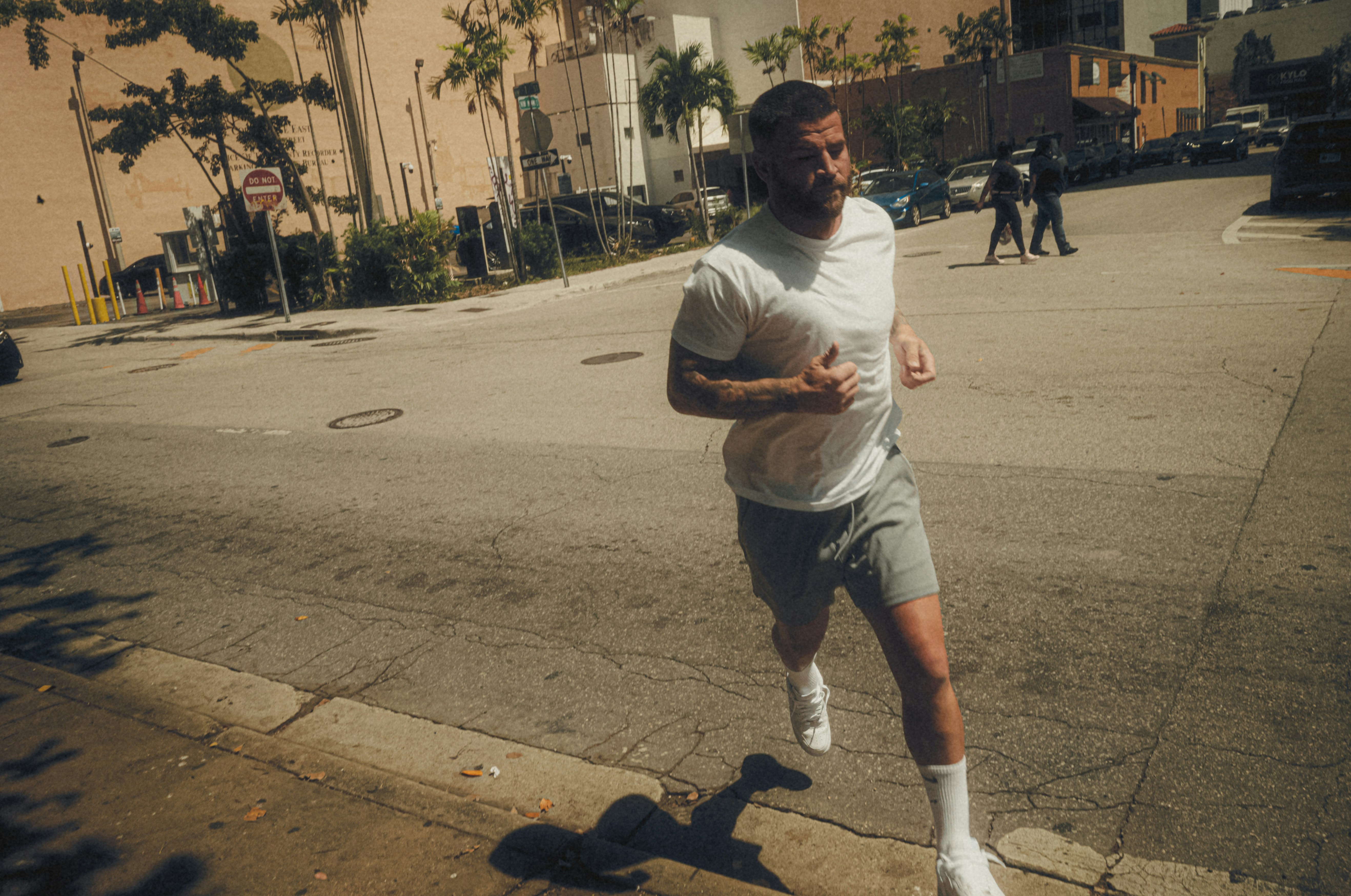 A man in athletic wear sprints along a sunlit street, showcasing determination amidst an urban backdrop. The scene captures the essence of city life and physical activity.