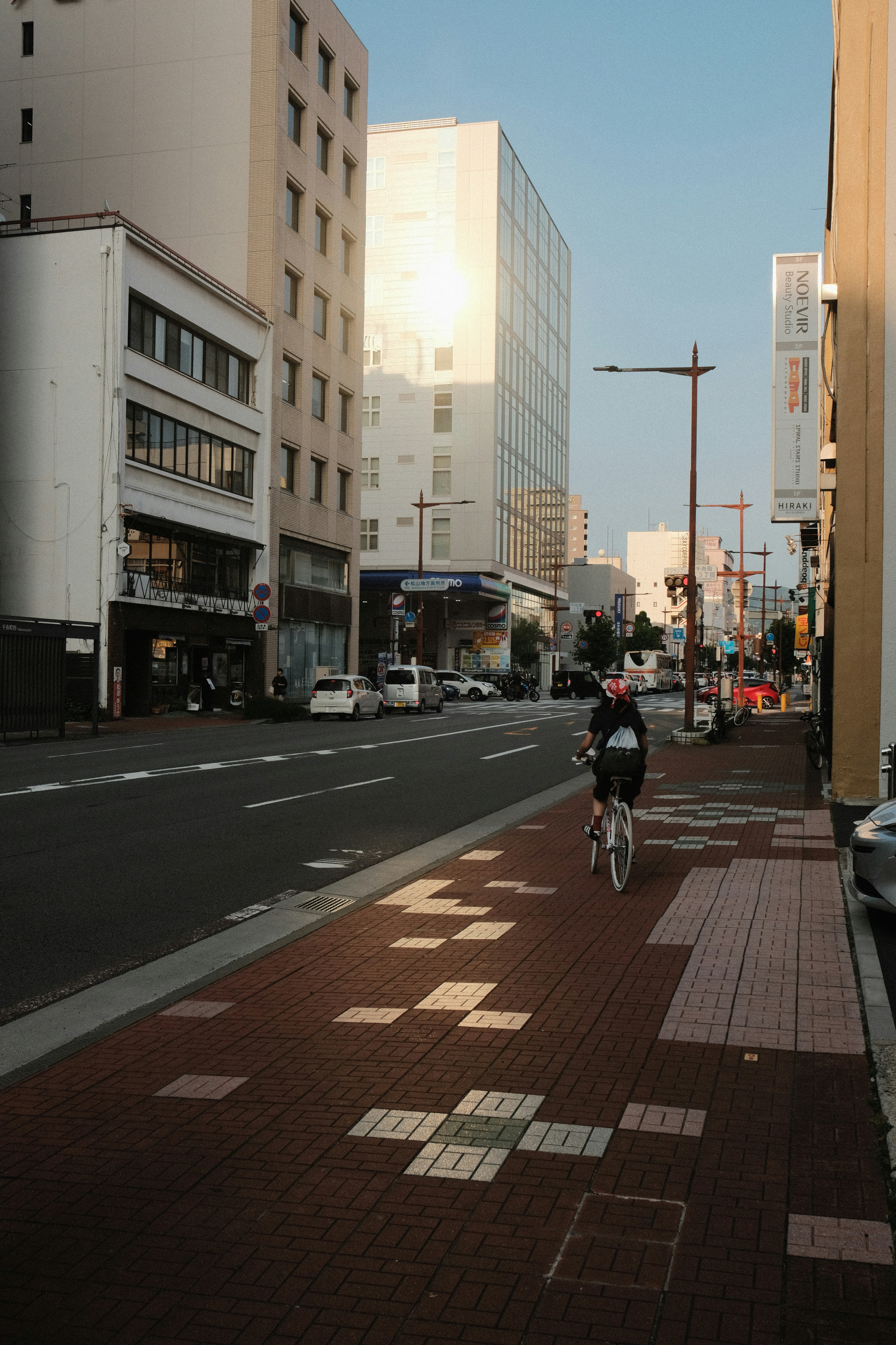 Cyclist navigating a patterned sidewalk amidst urban architecture during golden hour.