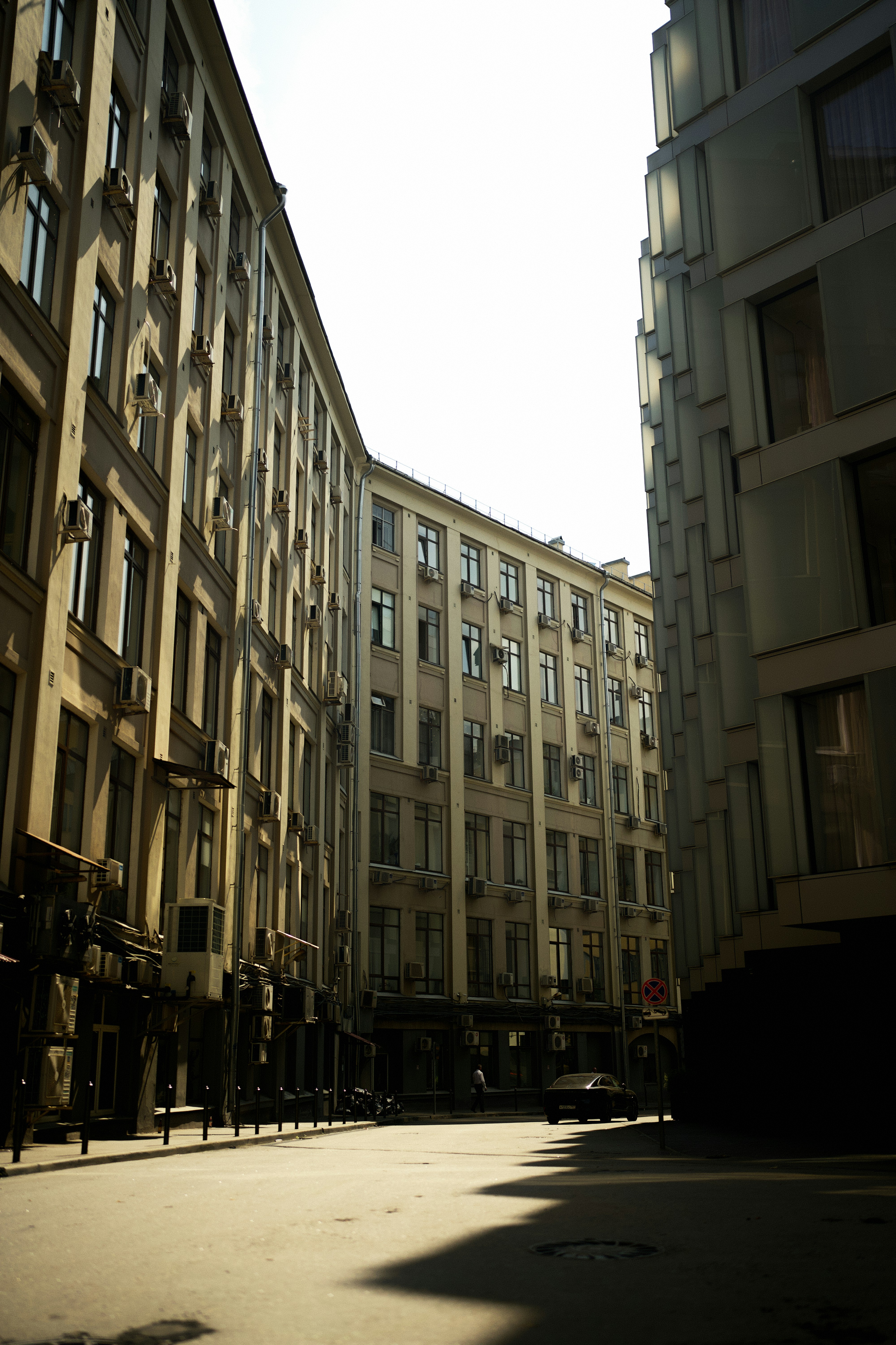 Narrow urban alley framed by contrasting architectural styles, showcasing a blend of modern and classic elements. The interplay of light and shadow adds depth to the scene.