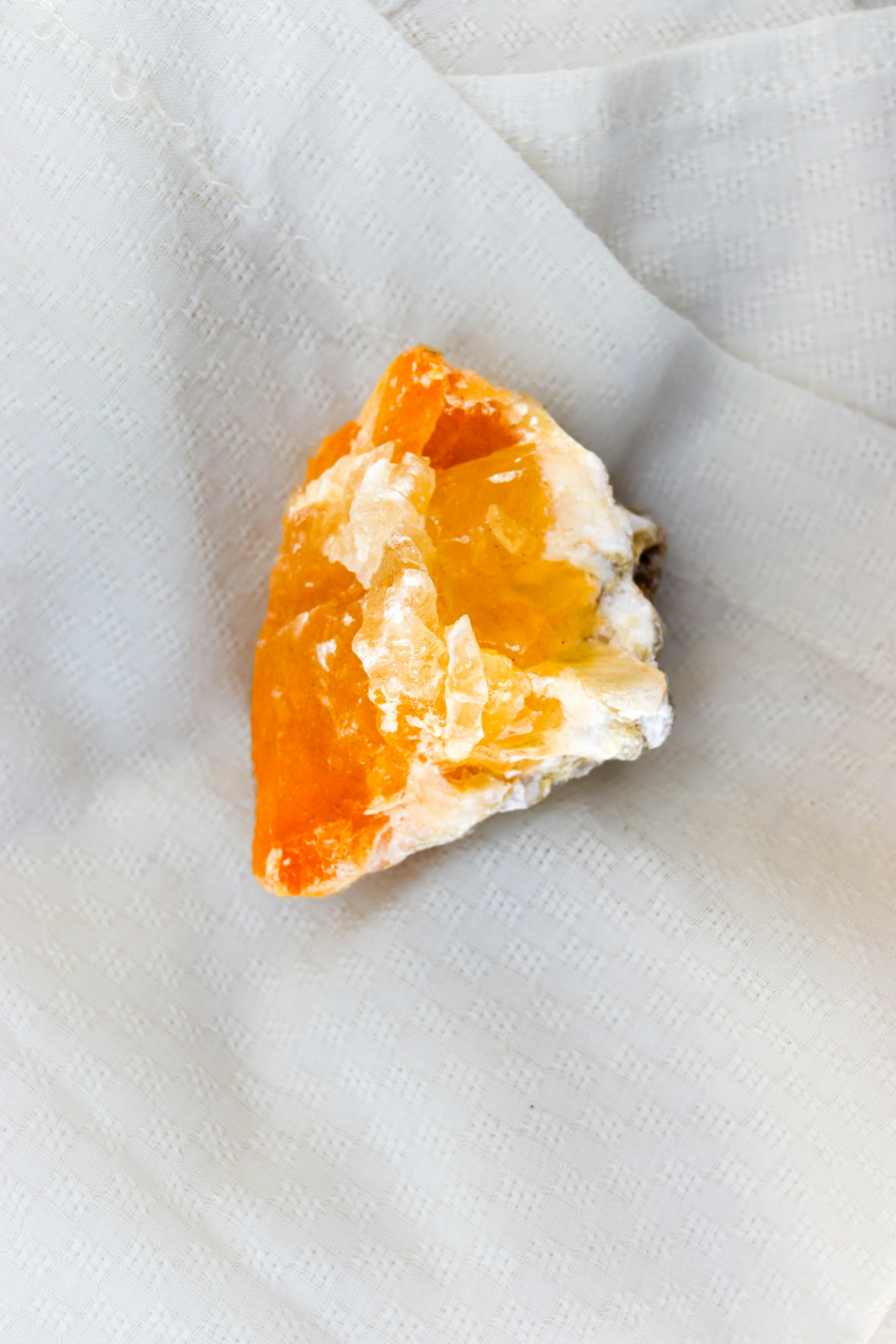 Orange calcite crystal rests on white cloth.