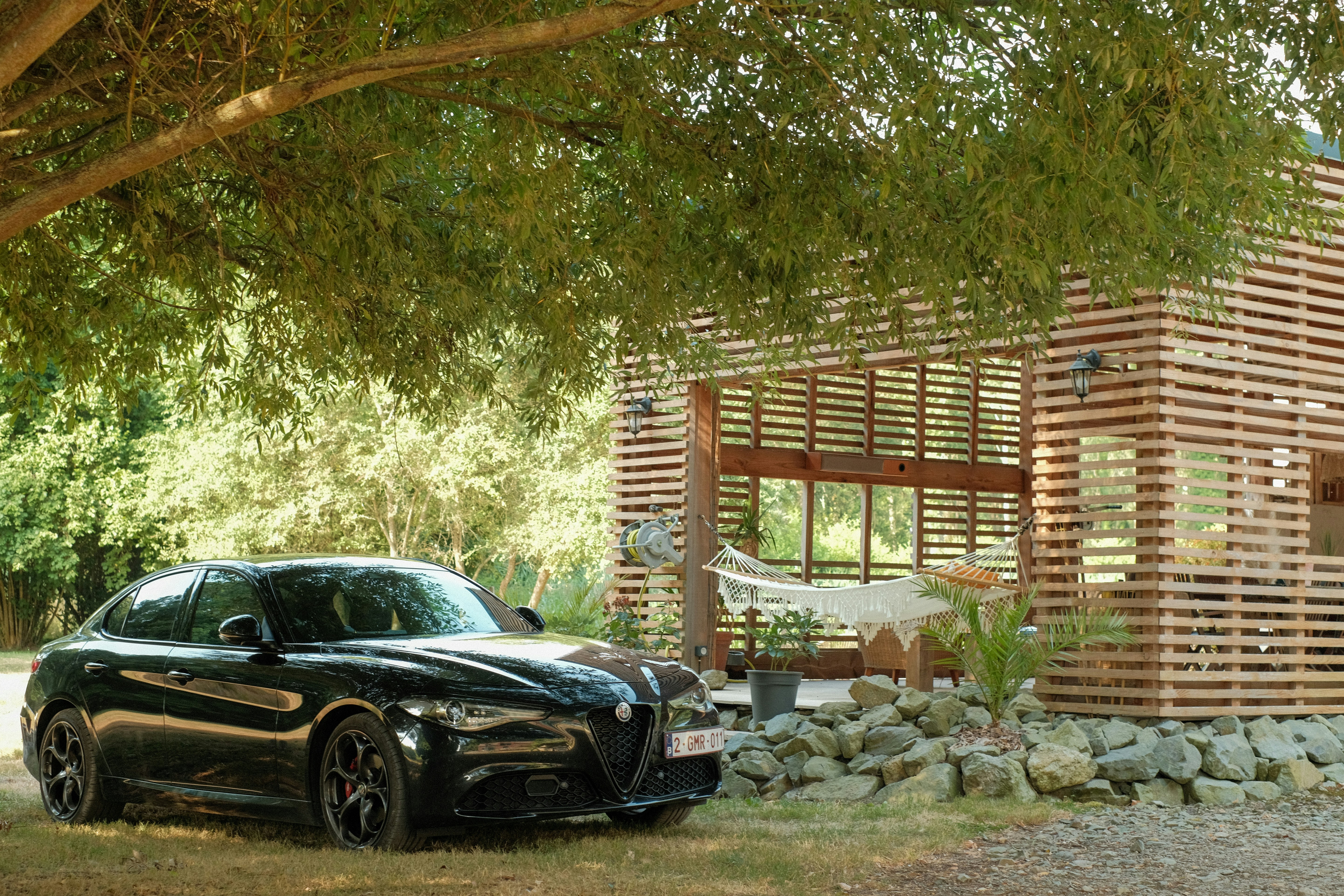 Sleek black sports car parked beside a contemporary wooden structure surrounded by greenery. The scene conveys a blend of luxury and tranquility.
