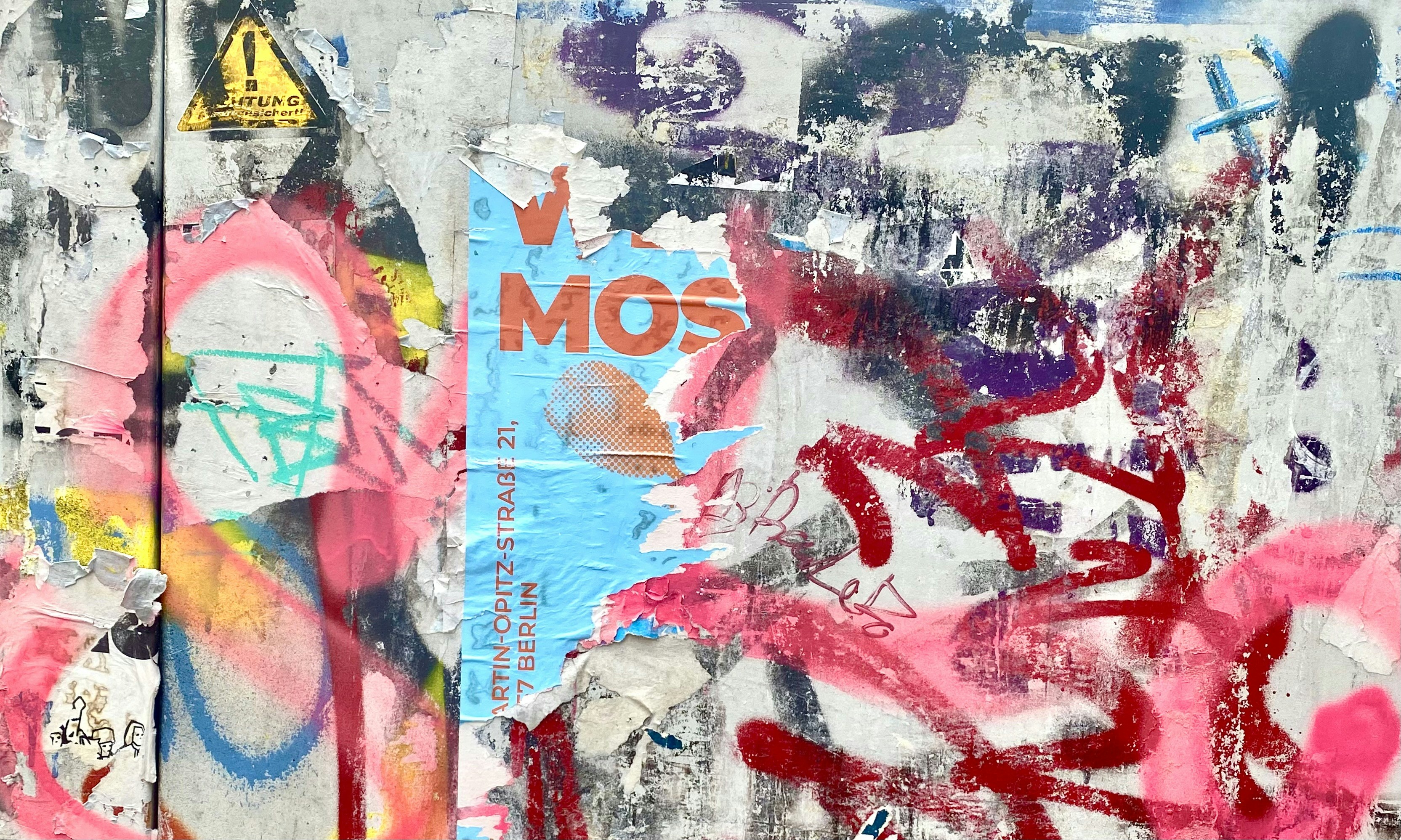 A vibrant wall covered in graffiti and posters, showcasing an eclectic mix of colors and urban art styles. The remnants of a poster hint at a past event in Berlin.