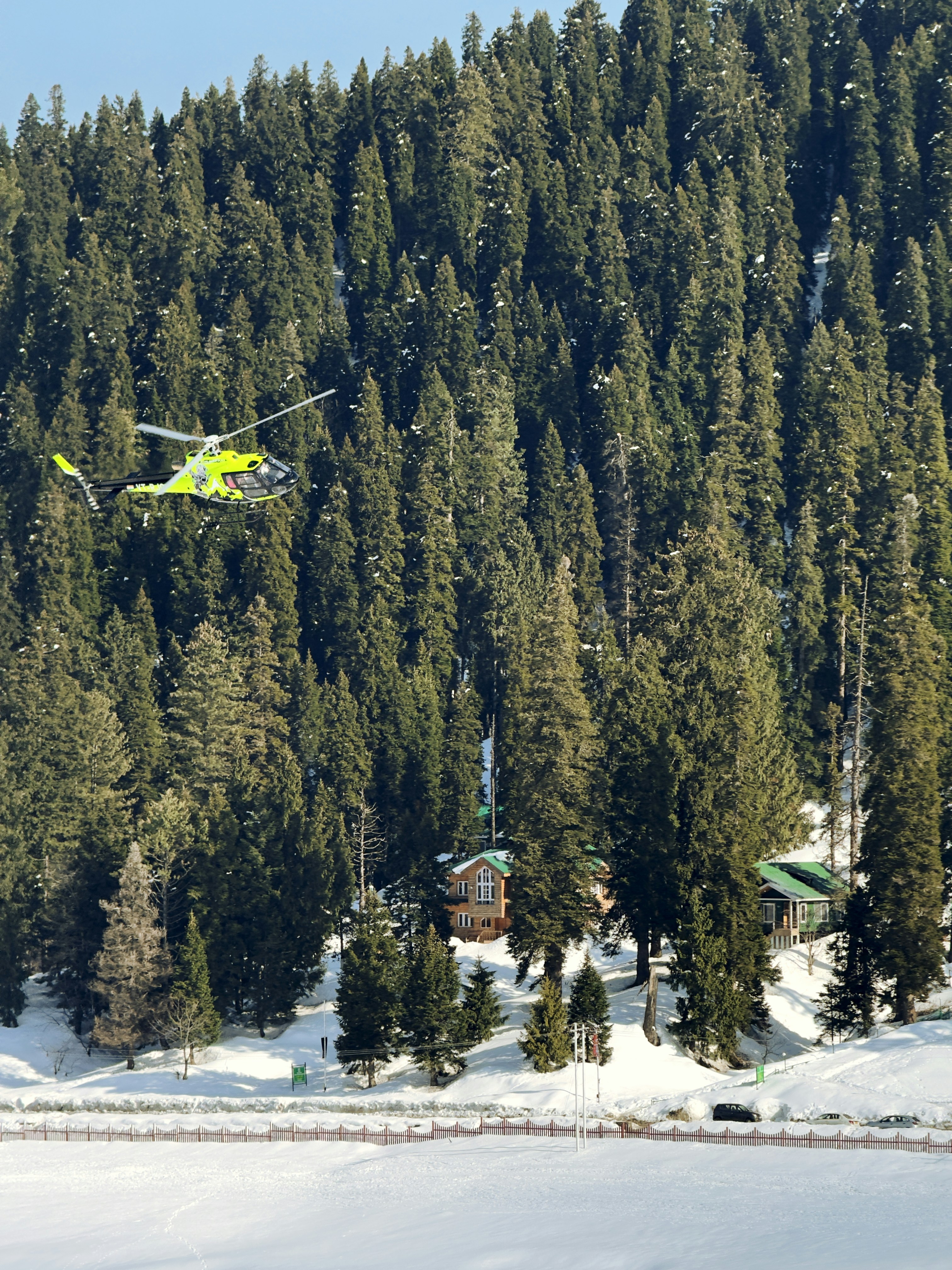 A helicopter flies over snow-covered trees.