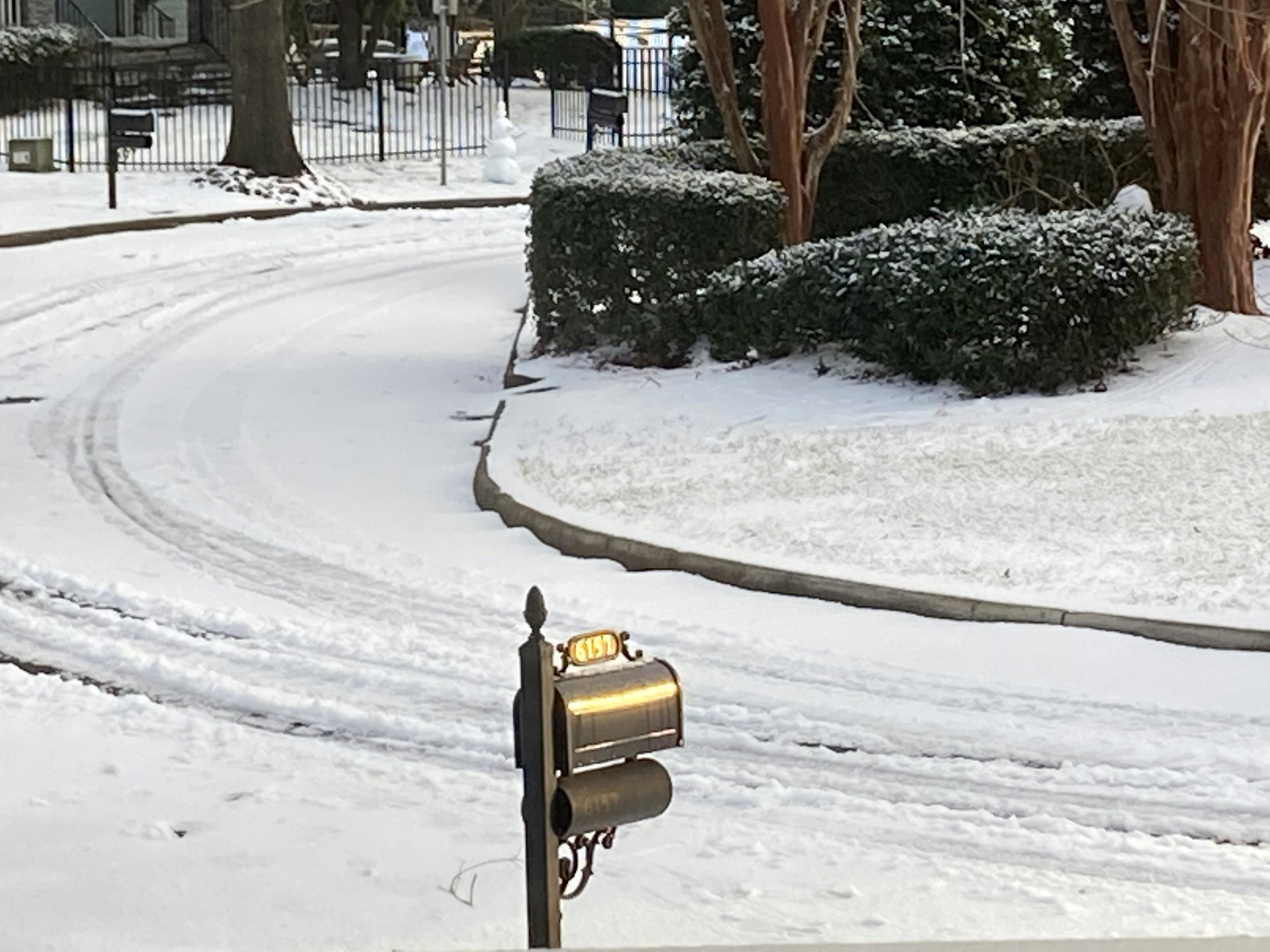 Sun on a black mailbox | Snow covers a street and greenery in winter.