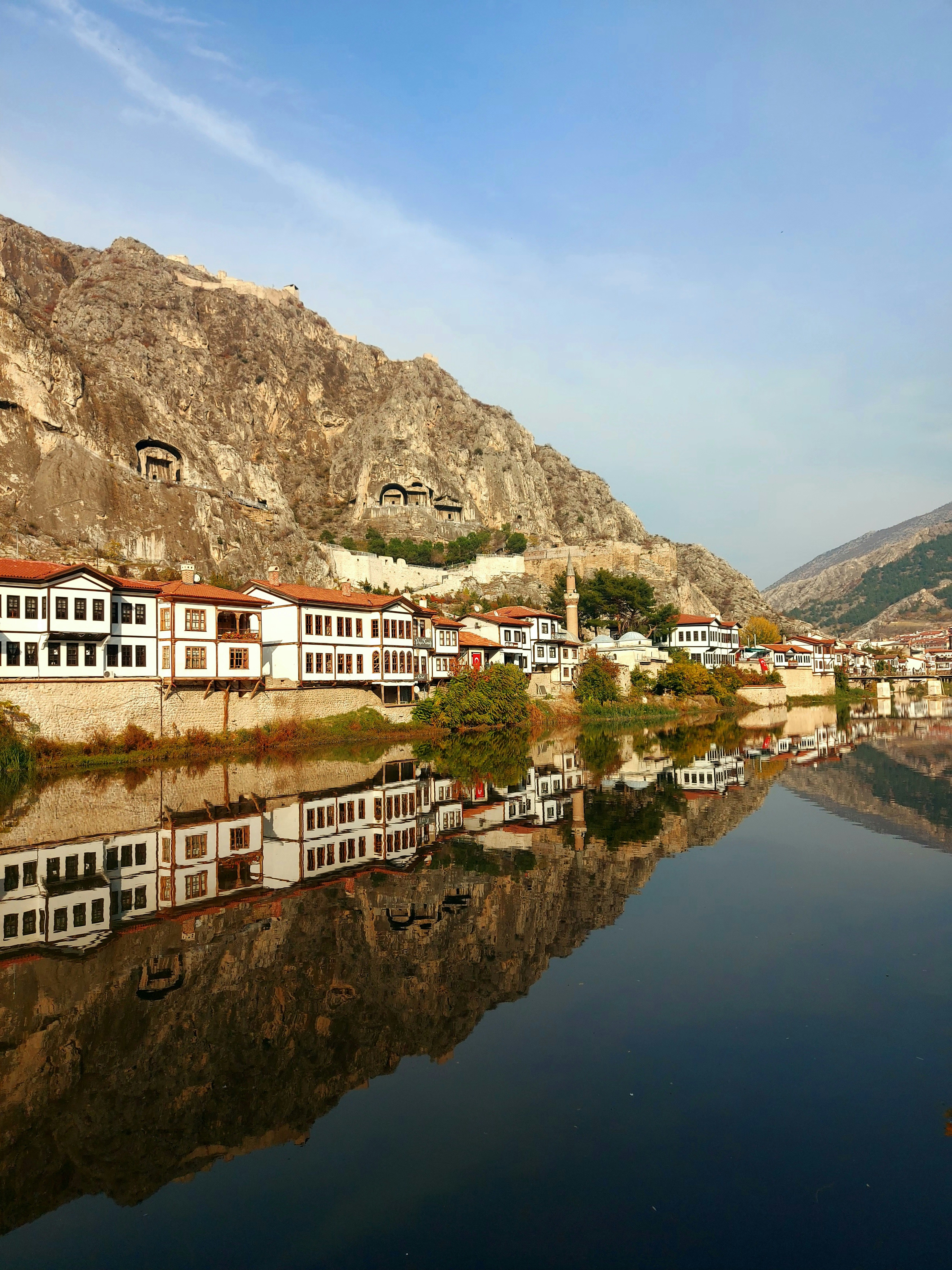 Houses reflect on the still river below a cliff.