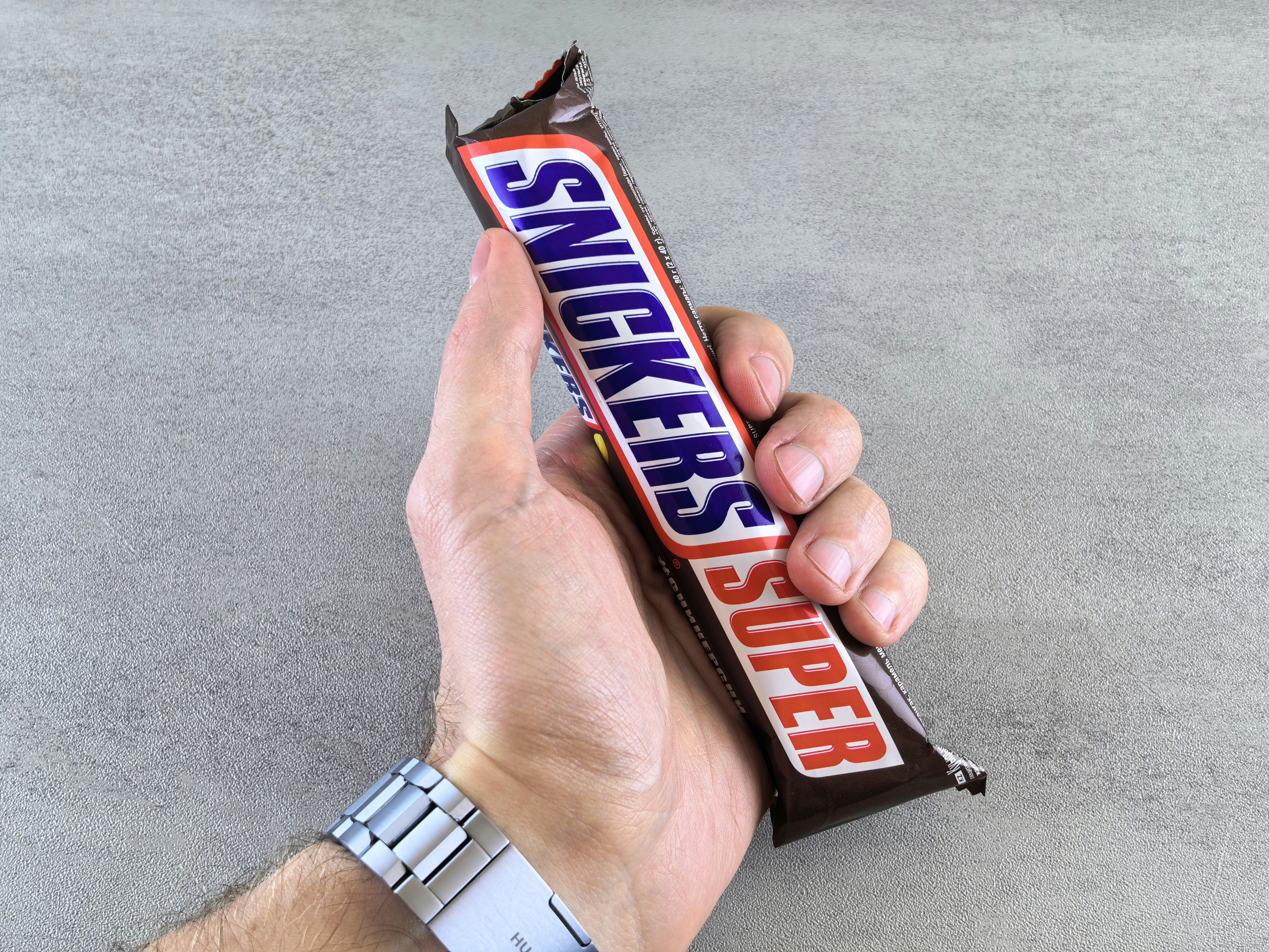 A hand holds a snickers super candy bar.