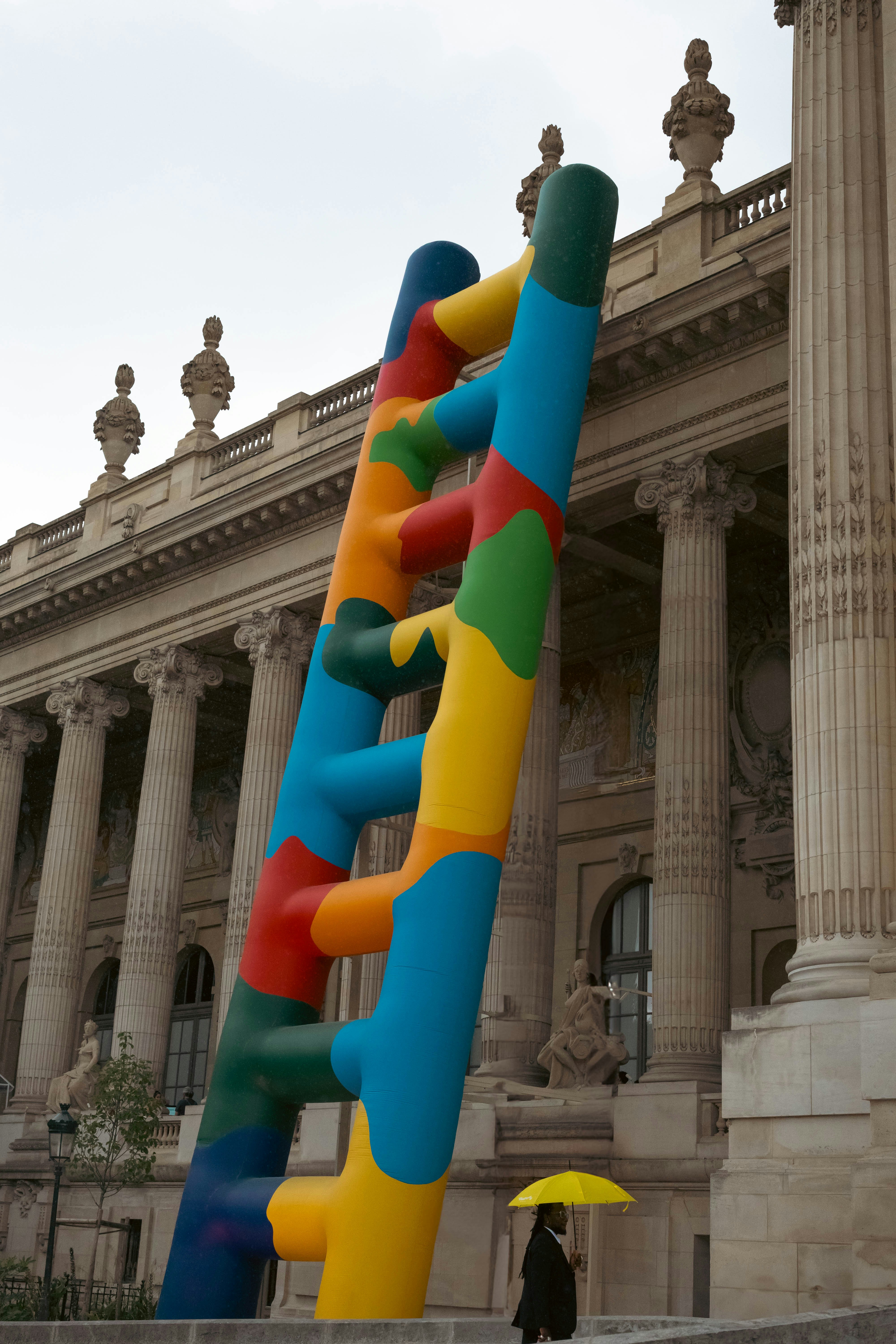 A colorful ladder sculpture stands before a building. photo – Free Art ...