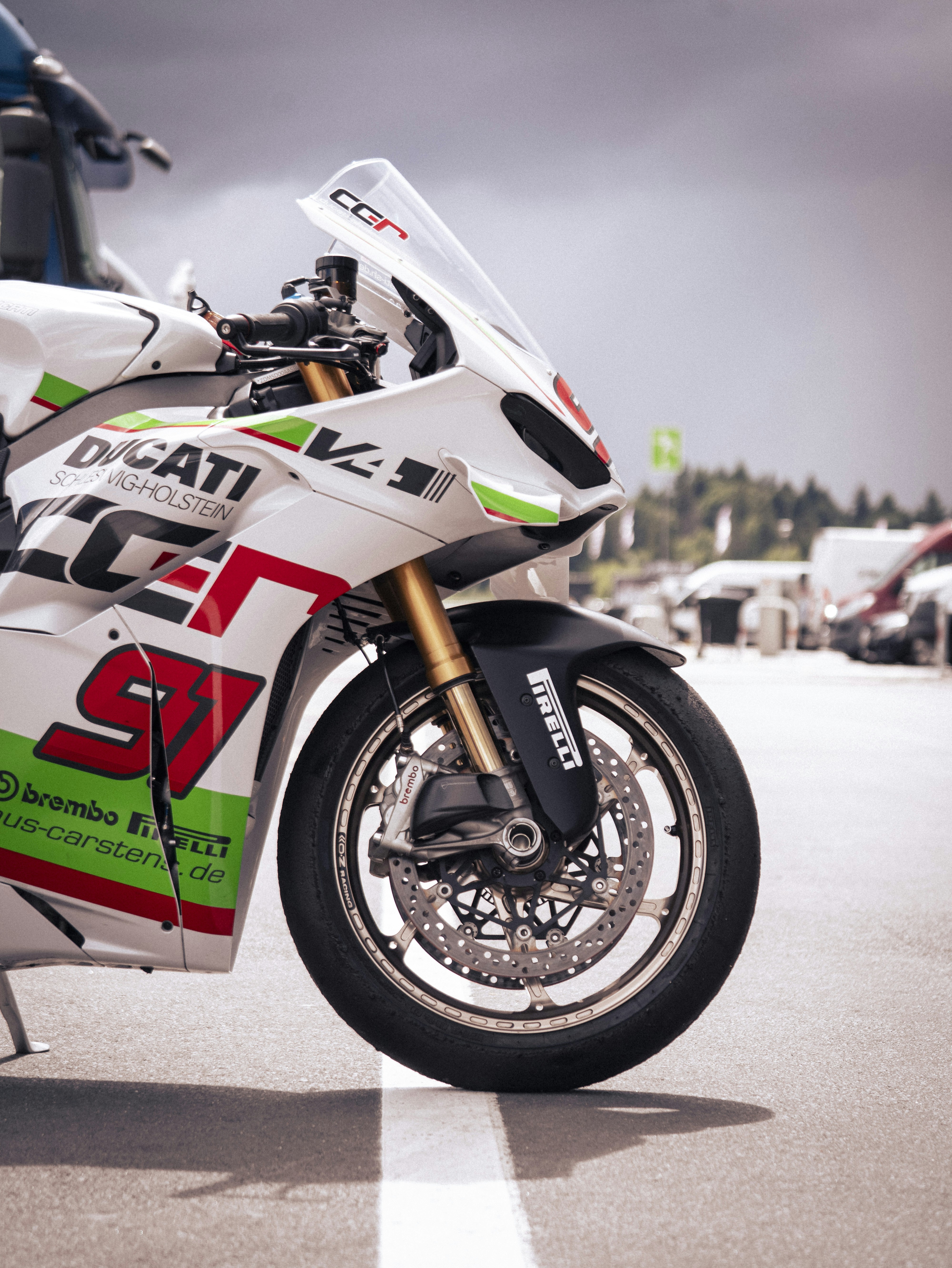 Close-up of a Ducati V4 motorcycle showcasing its sleek design and intricate components. The focus is on the front wheel and suspension system.